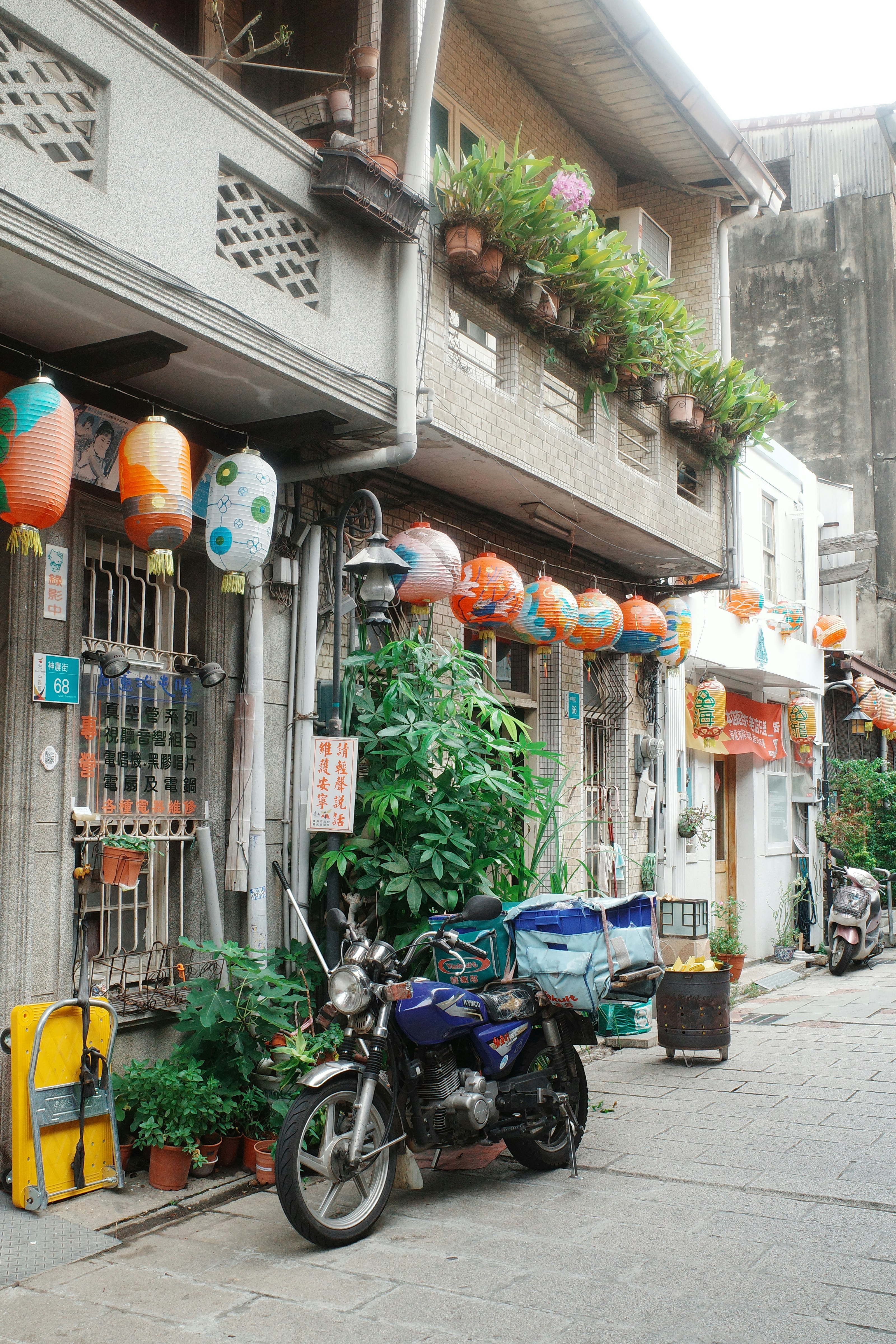Motorcycle parked on a narrow street with lanterns.