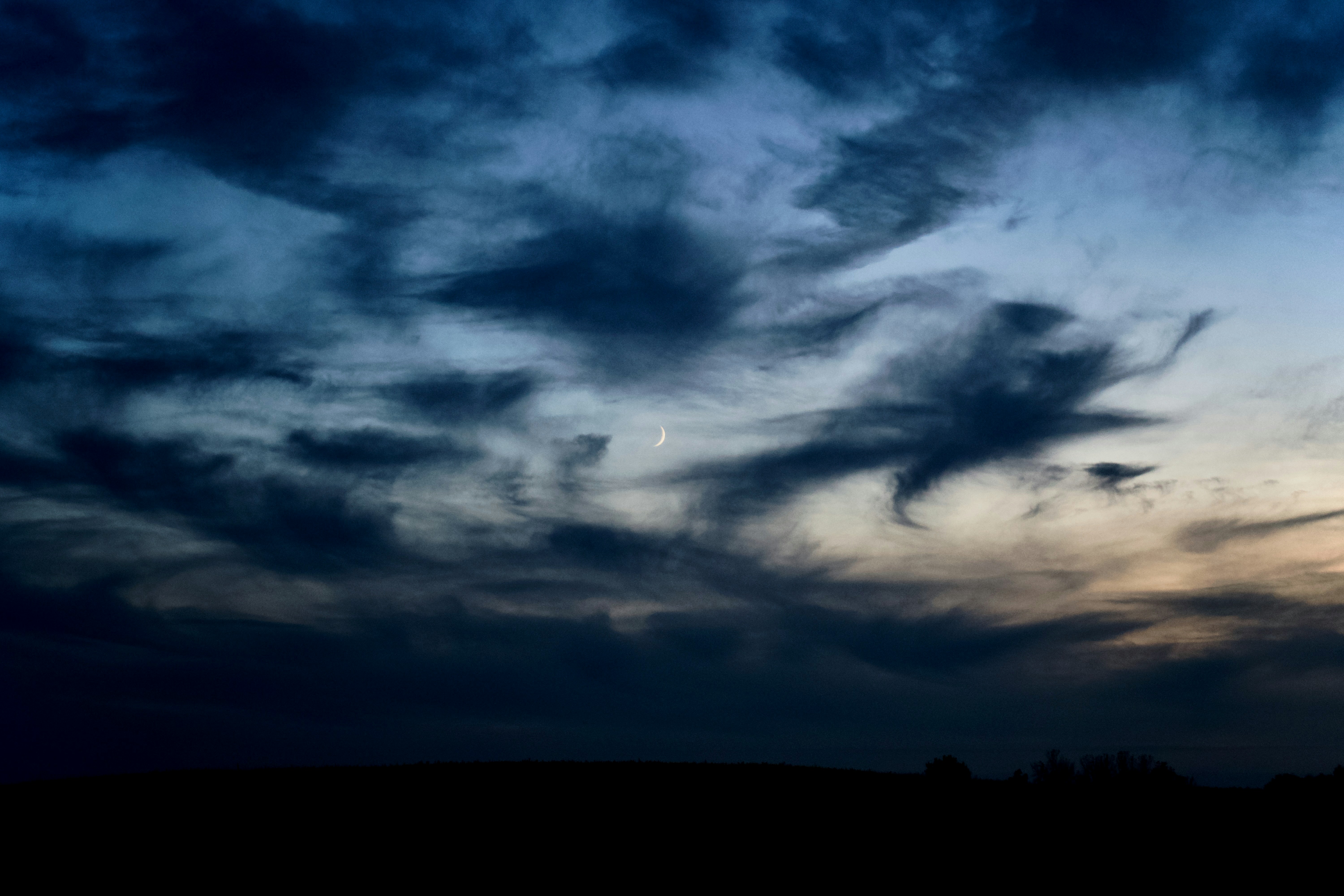 Dark, dramatic clouds at dusk with a sliver of moon.