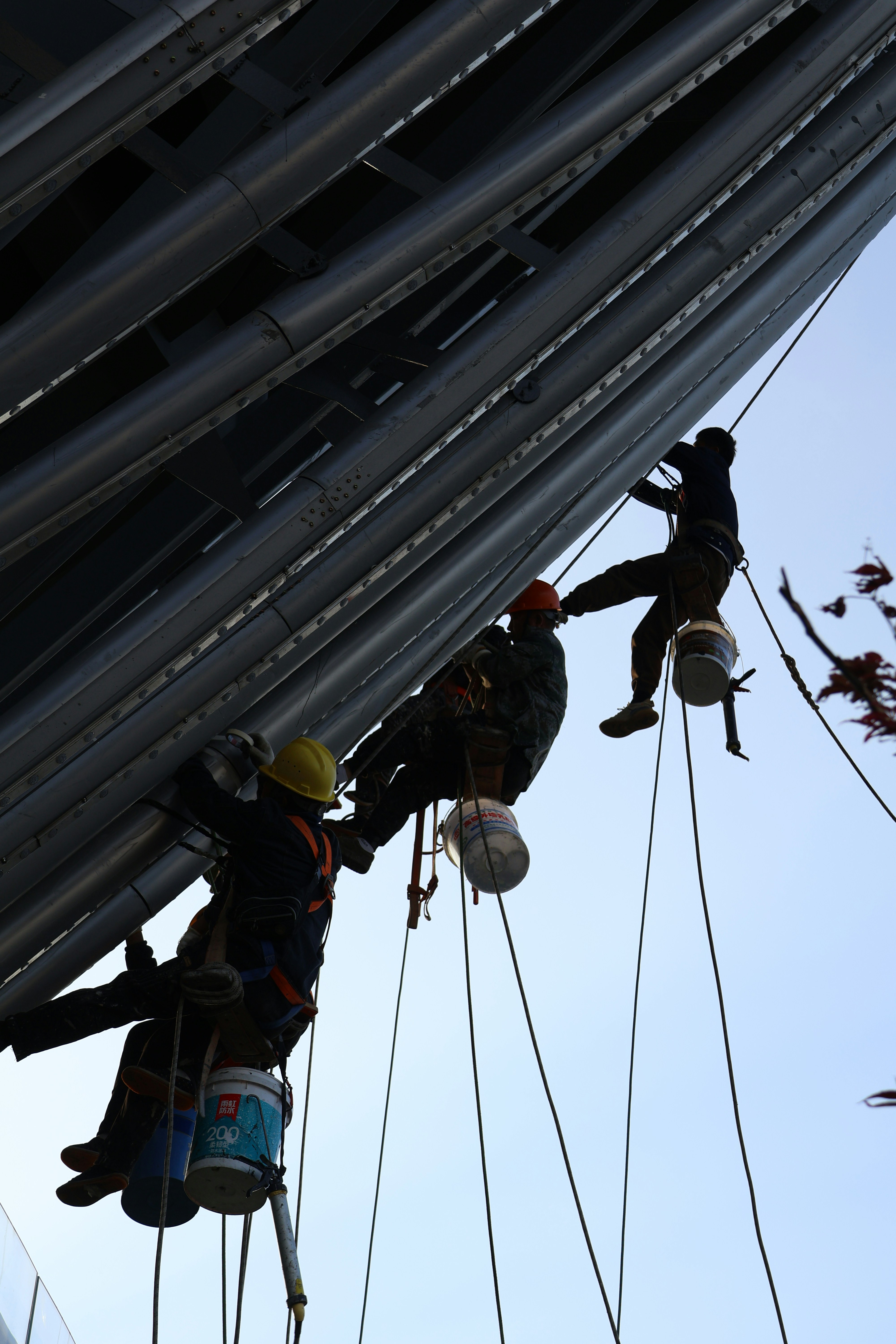 Workers suspended by ropes painting a tall structure