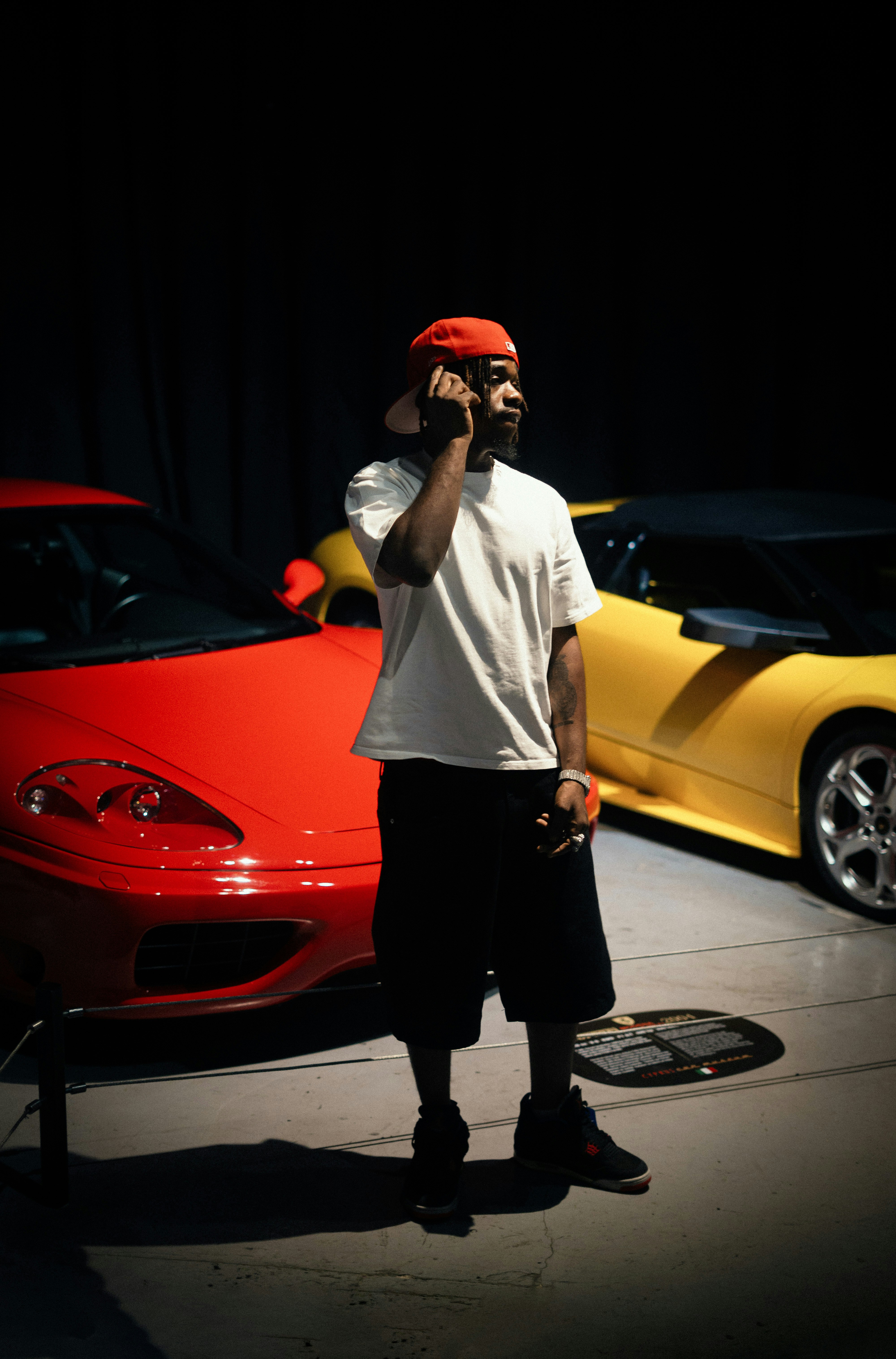 Man in red hat talking on phone near cars