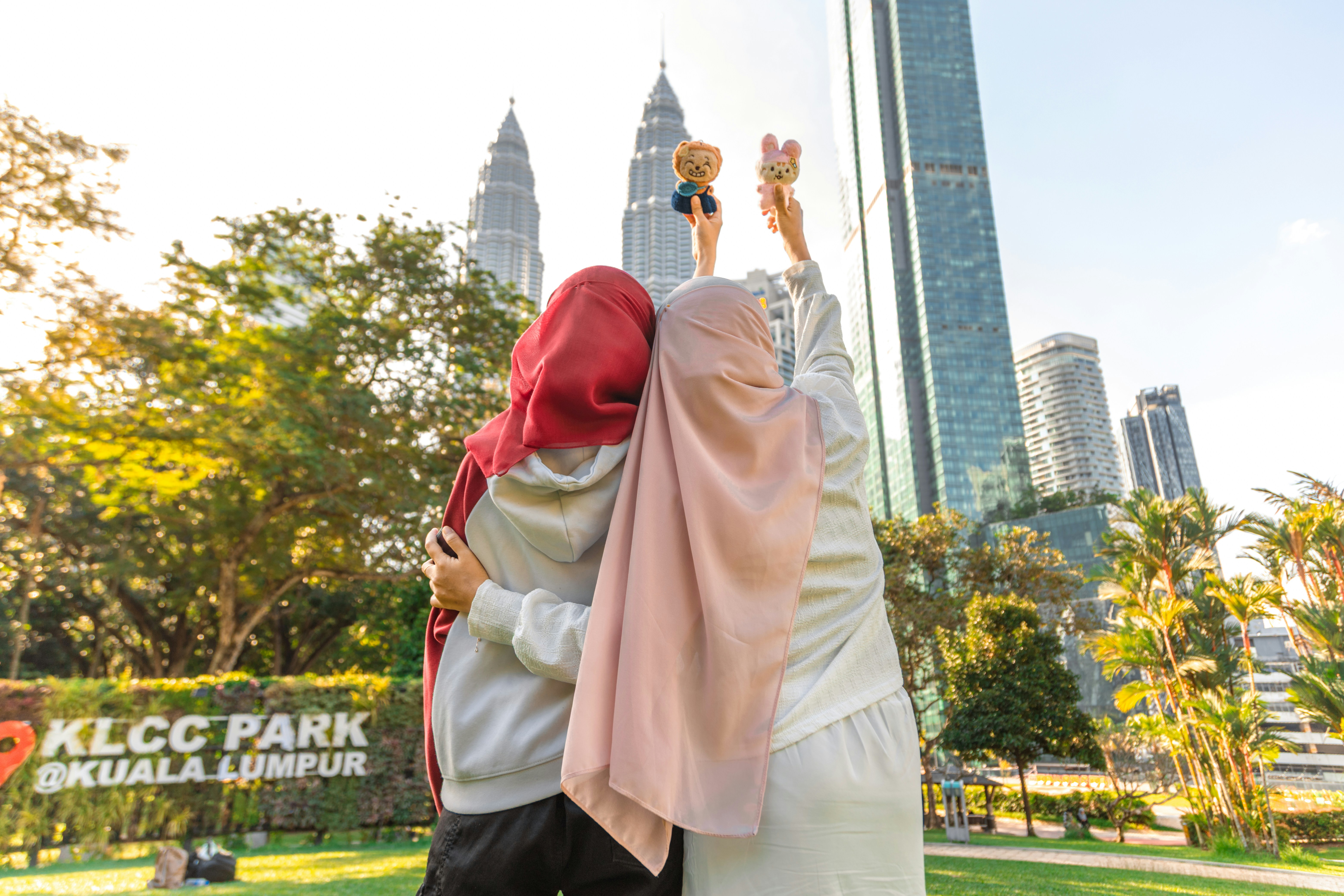 Two women in hijabs taking a selfie with petronas towers.