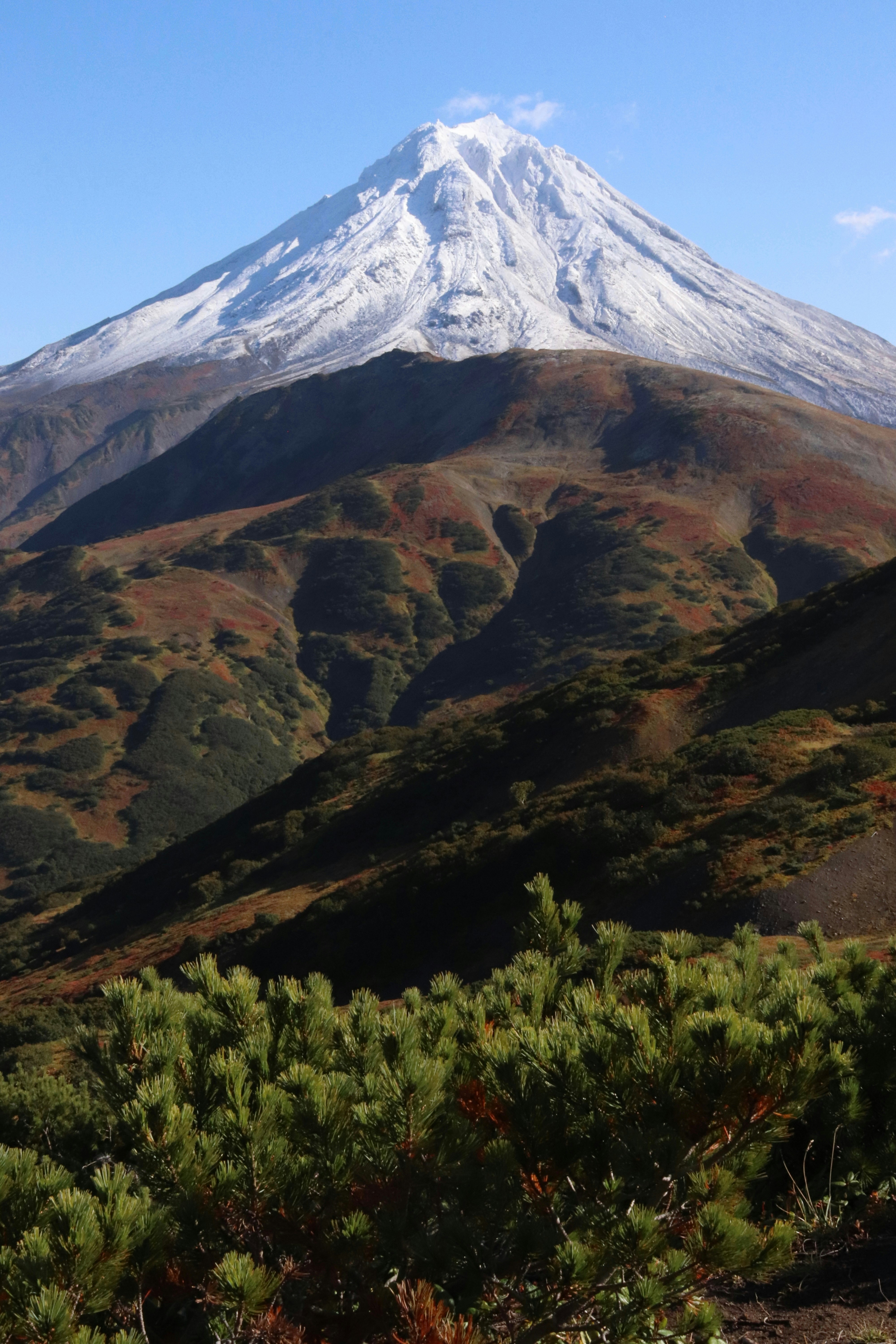 Snow-capped volcano rises above autumn-colored hills.