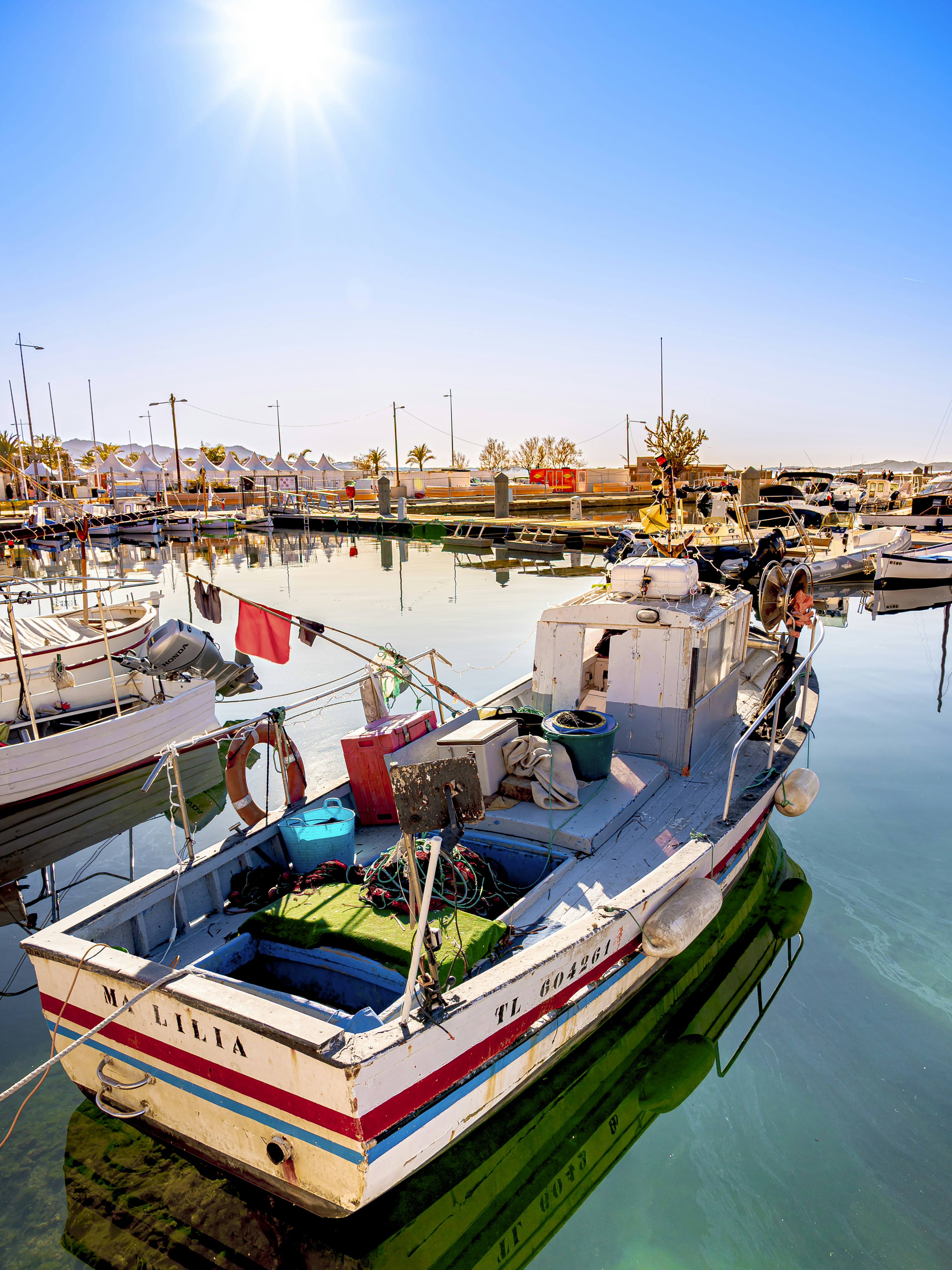 Fishing boat docked in a sunny harbor with clear water.