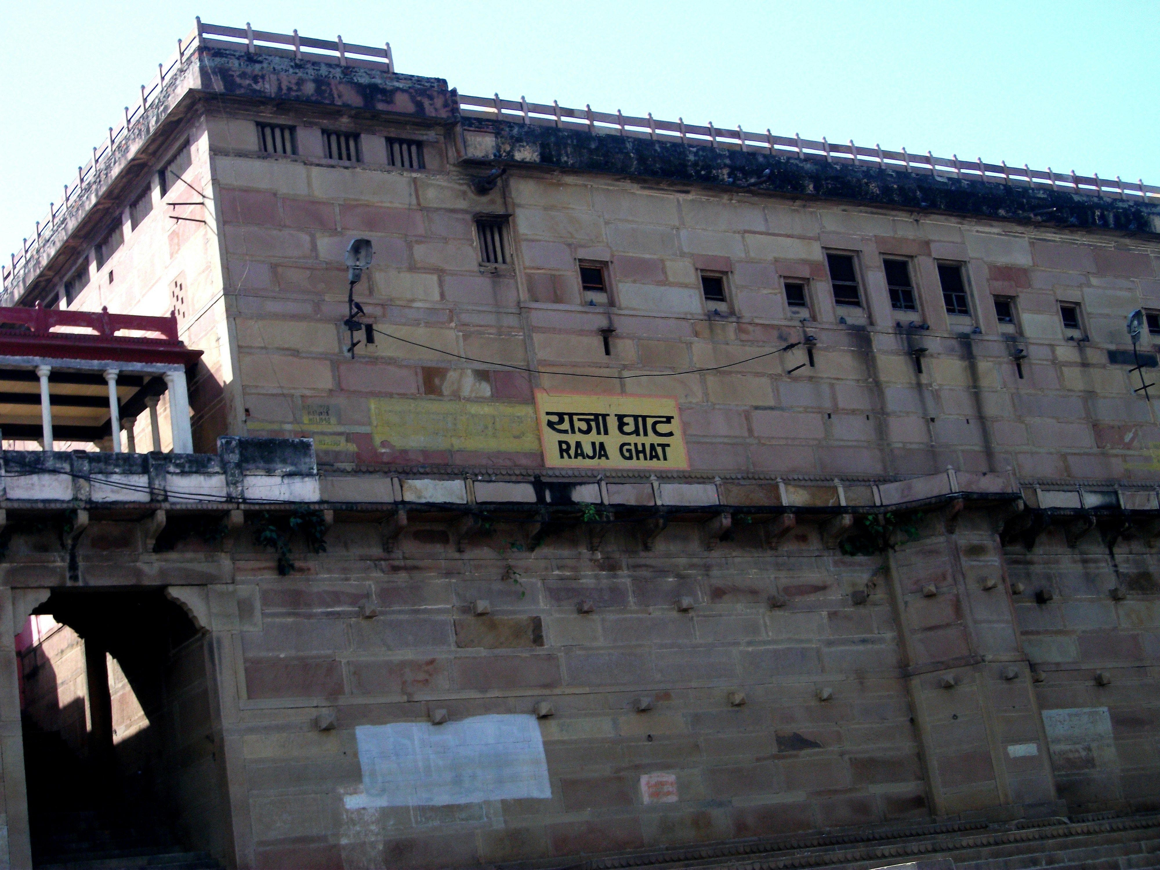 Varanasi is the first and last City on Earth. Every Day Many Pilgrims and Devotees from All Around the World Visit Varanasi (Khaasi). People Take Bath on the Ghats of Varanasi in the Holy River Ganga and Worship the Destroyer Shiva. Kala Bhairav is the Protector of this City. | Stone building with yellow sign saying "ram ghat"