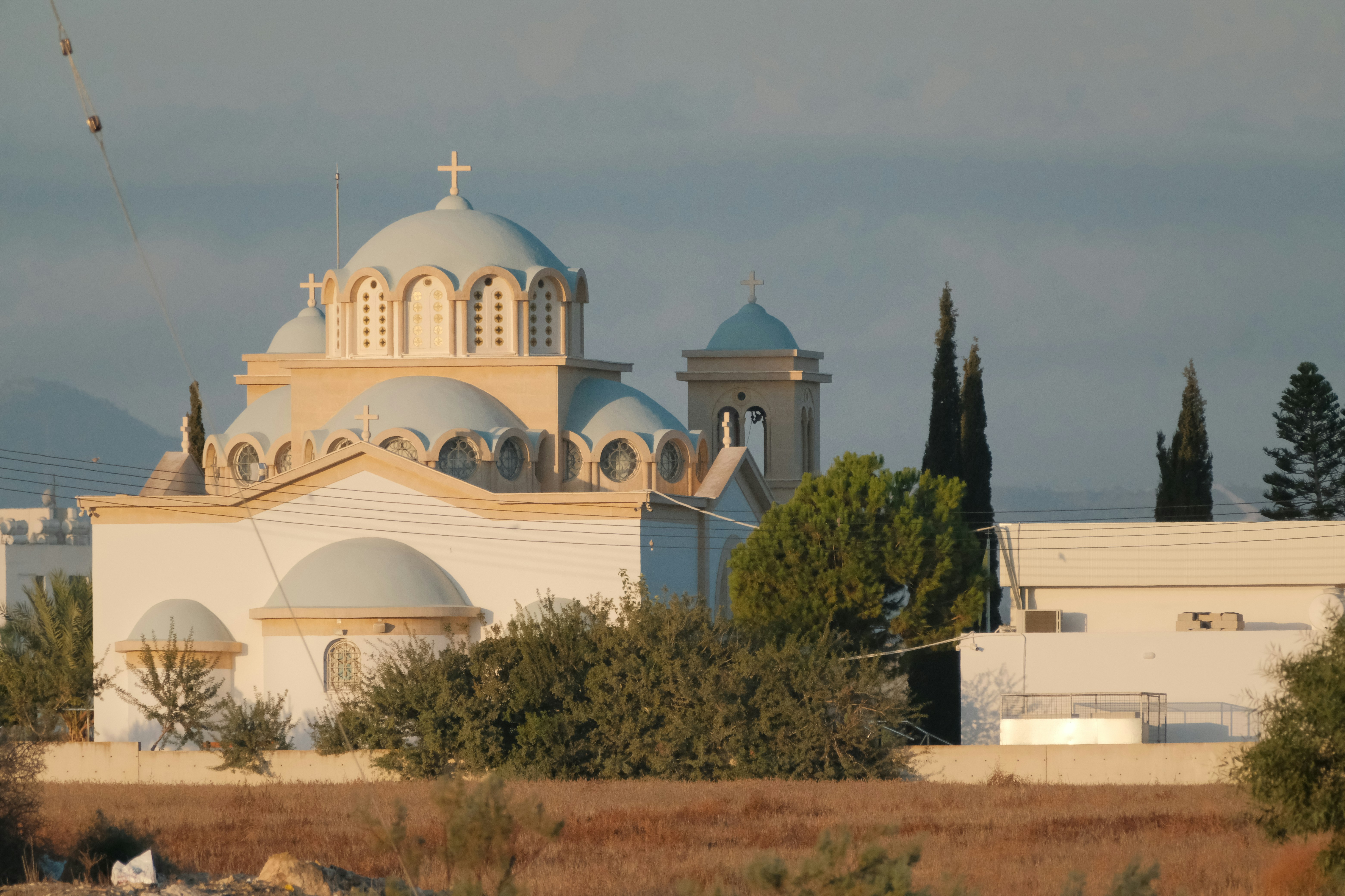 A white church with blue domes and cypress trees.