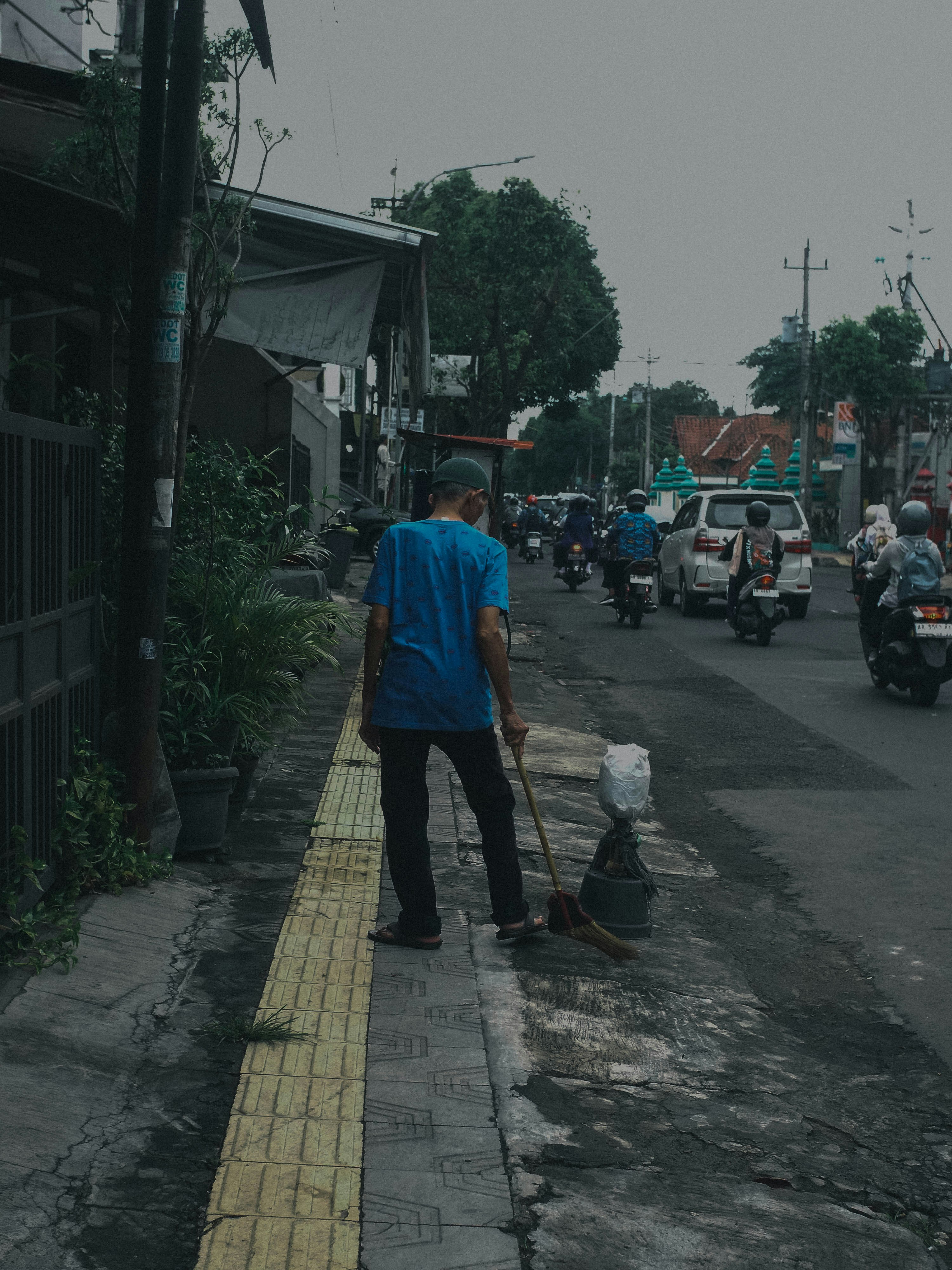 Man sweeps sidewalk next to busy street