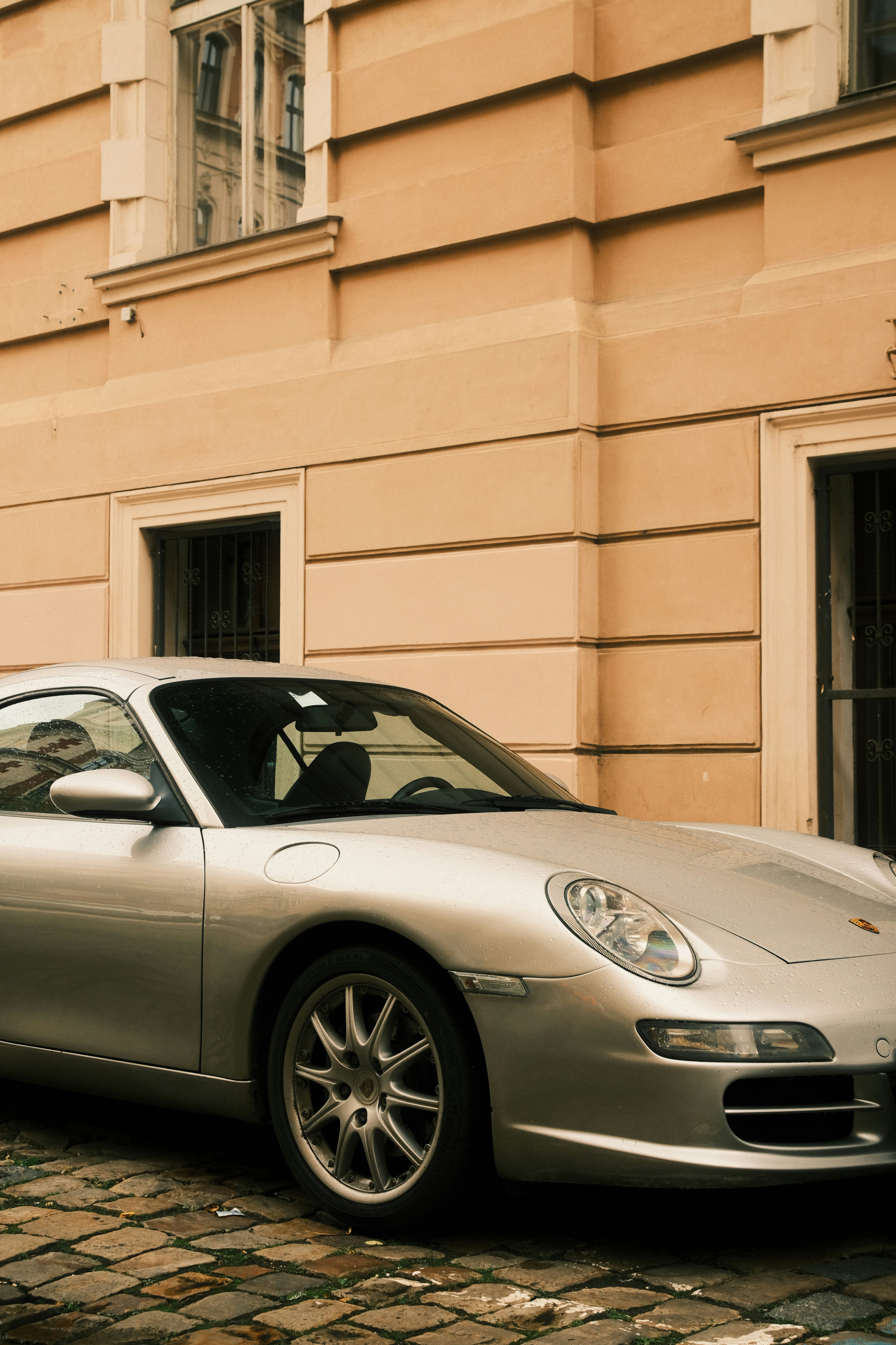 Porsche 911 Carrera (996) | Silver sports car parked on cobblestone street.