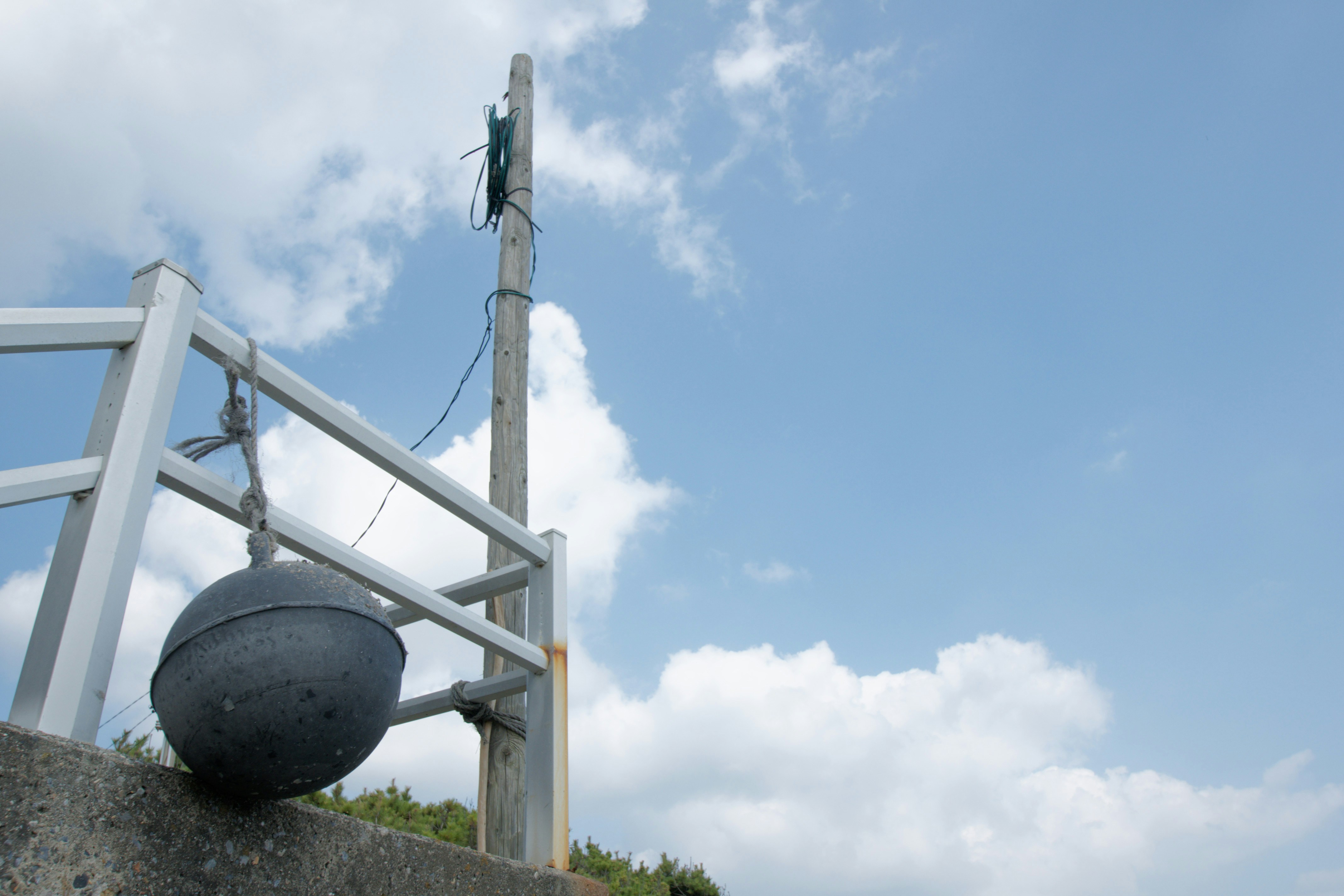 A gray buoy hangs from a railing near a pole.