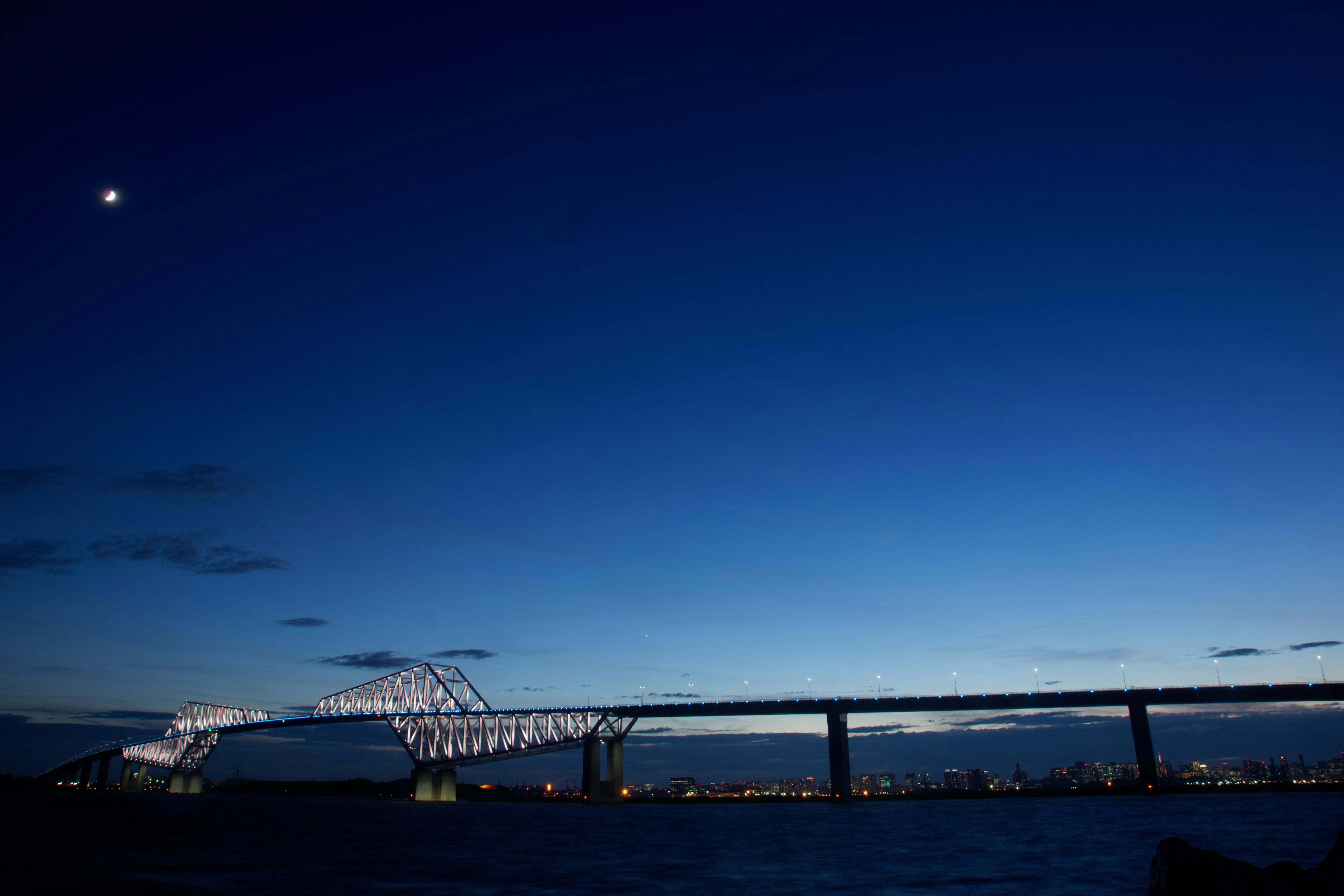 東京ゲートブリッジ | Bridge illuminated at night over water with moon.