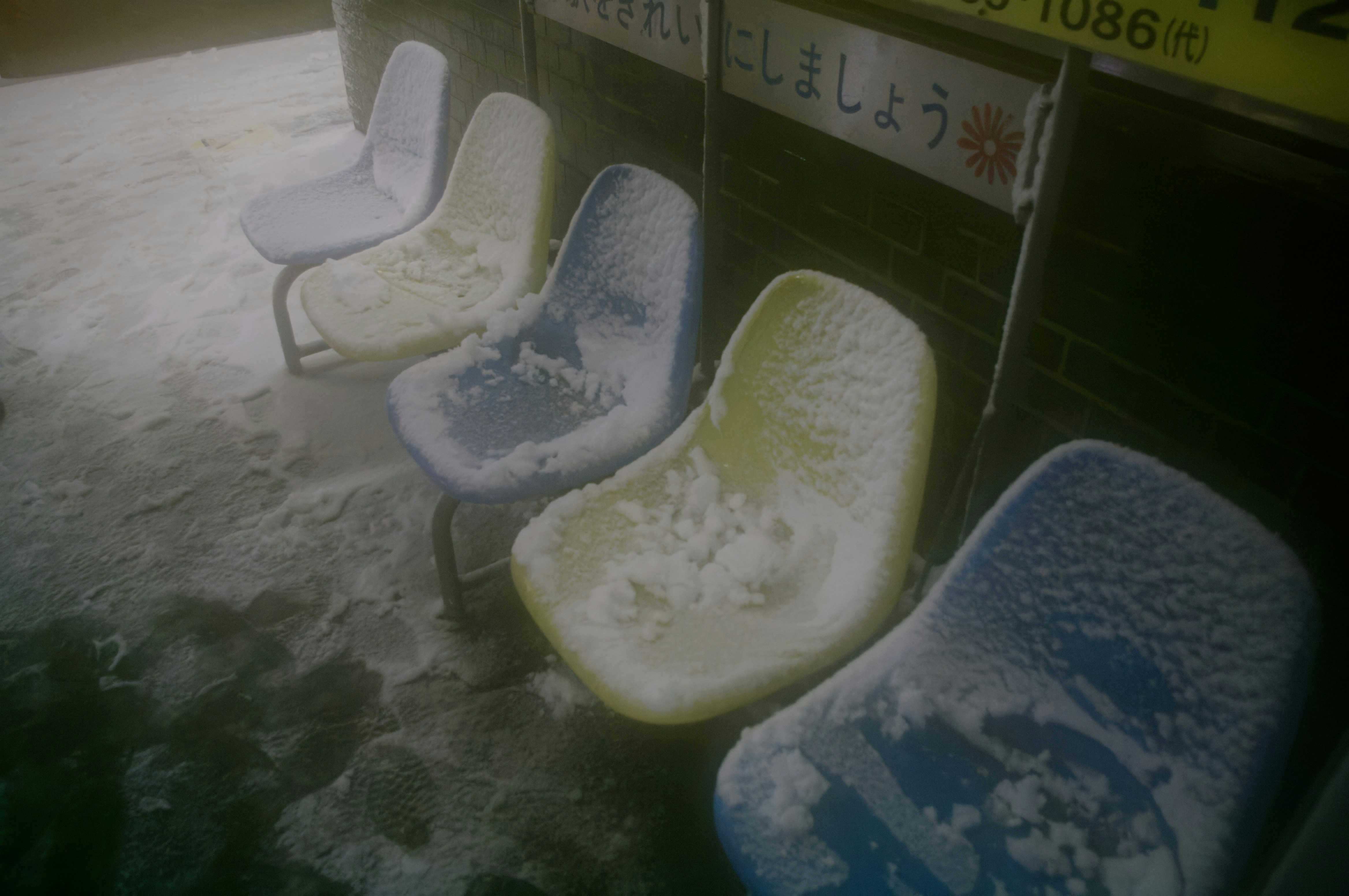 Empty, snow-covered seats at a bus stop, evoking a sense of solitude in a winter landscape.