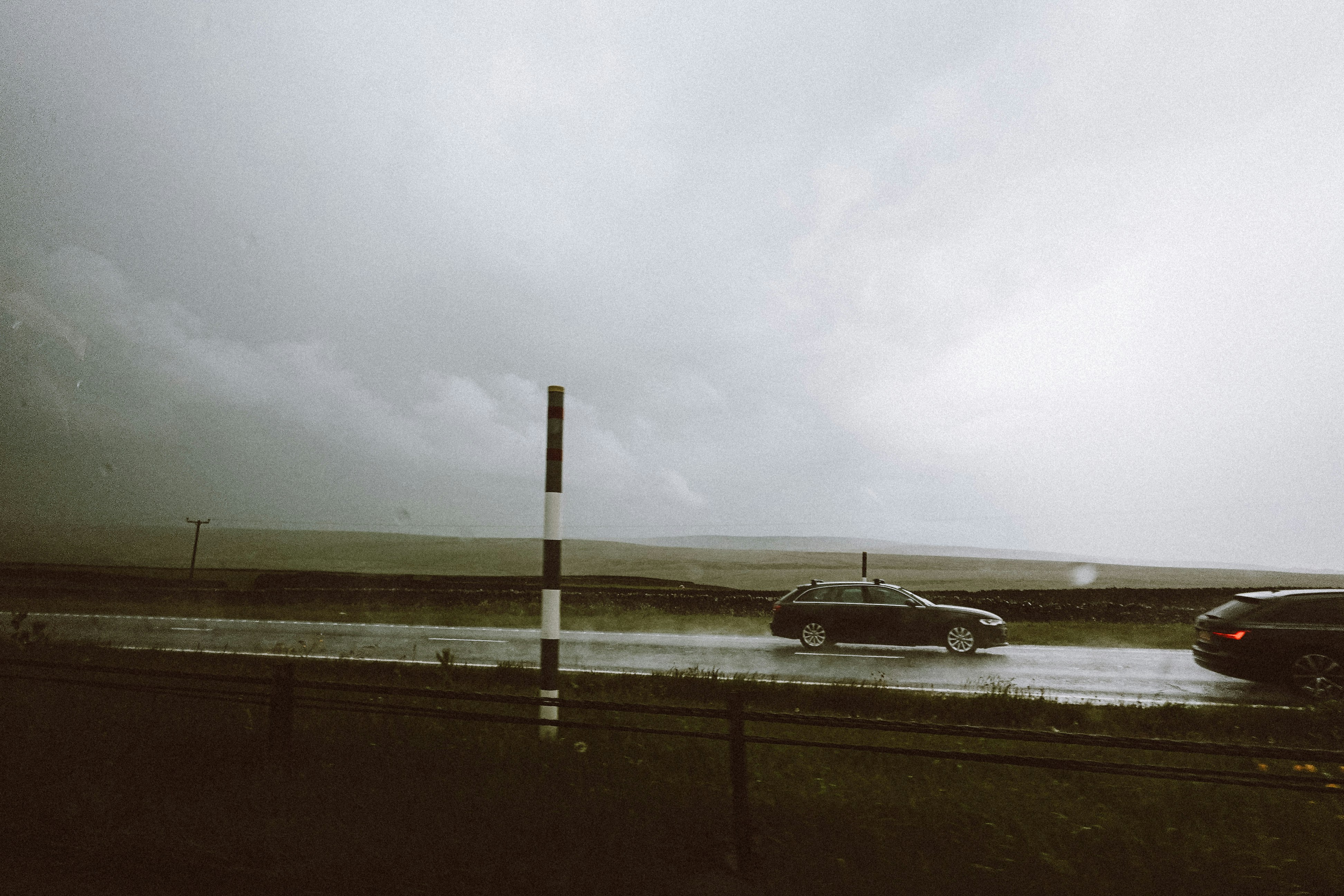 Cars driving through a flooded road under stormy skies.