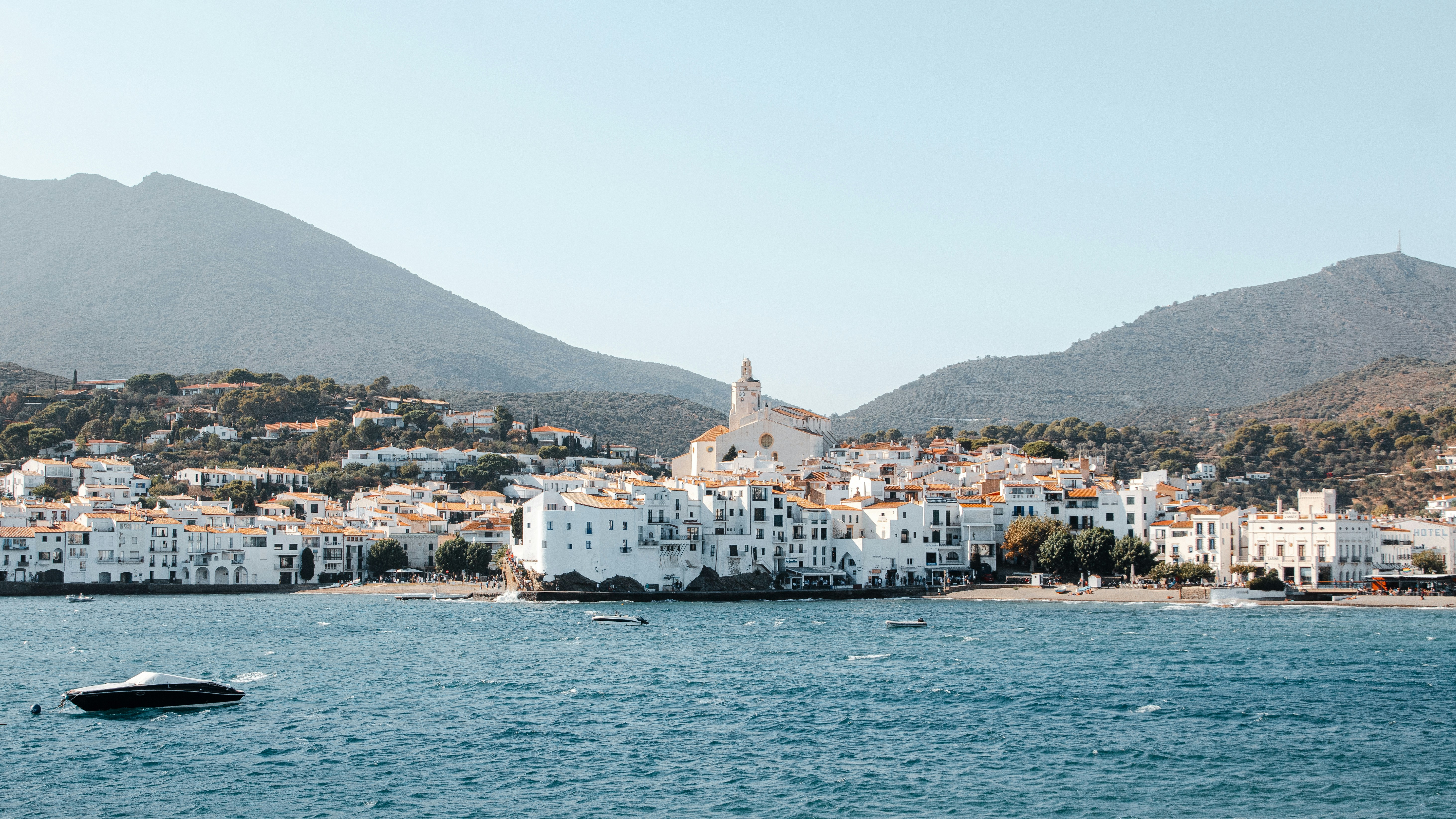 White buildings on the coast with mountains behind.