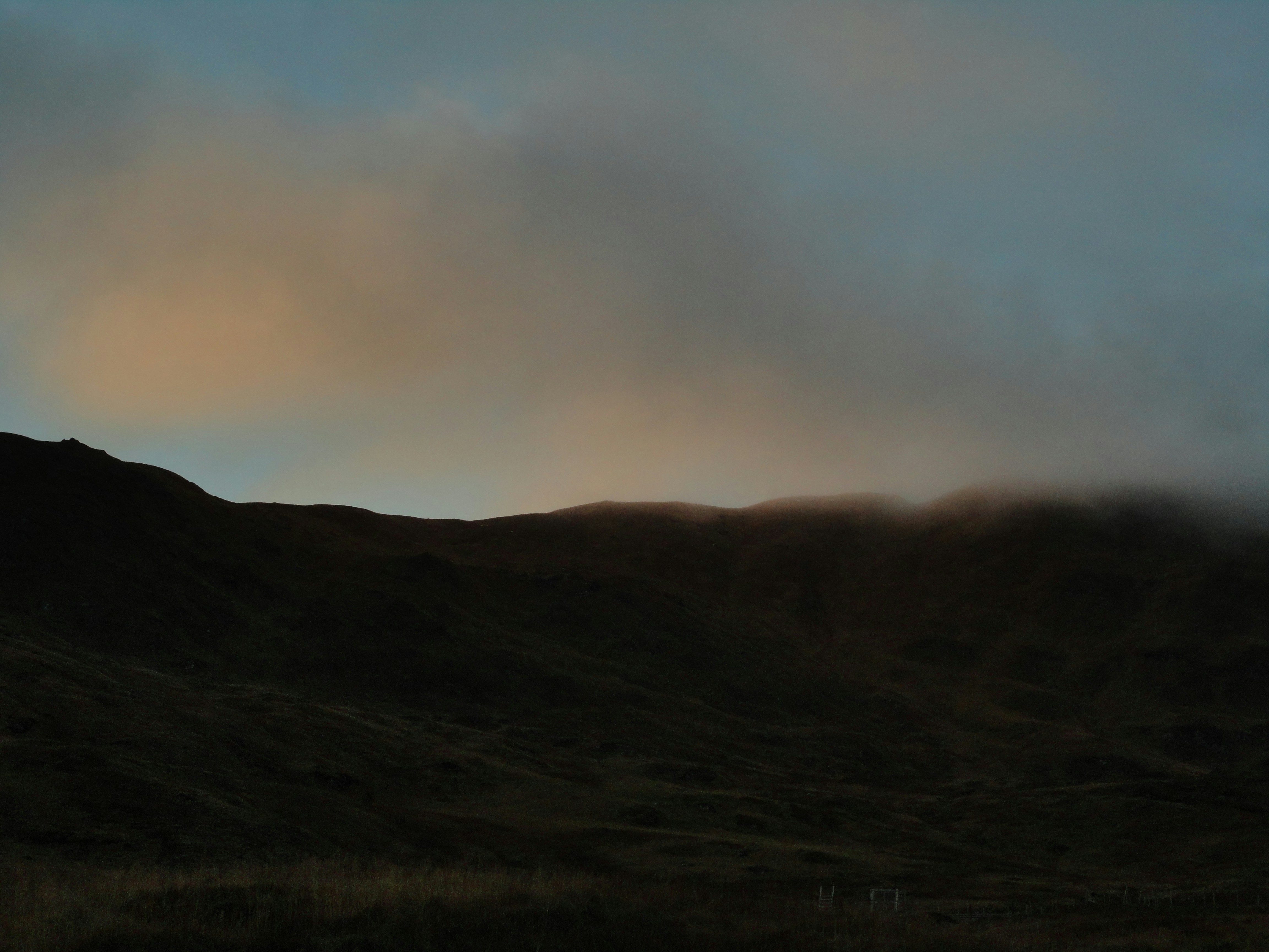 Silhouetted hills under a twilight sky, with soft clouds illuminated by fading light.