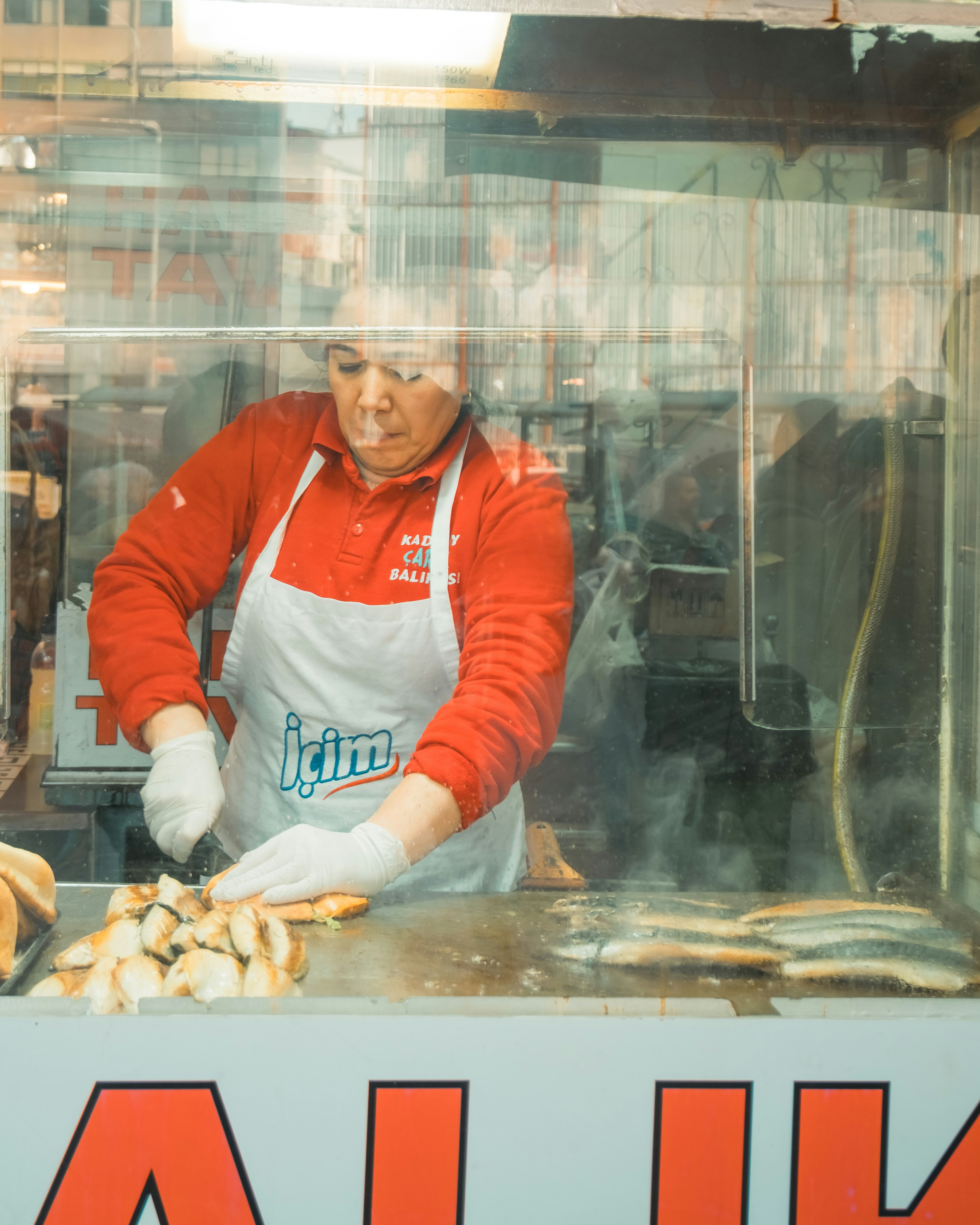 A person preparing food behind a glass counter.