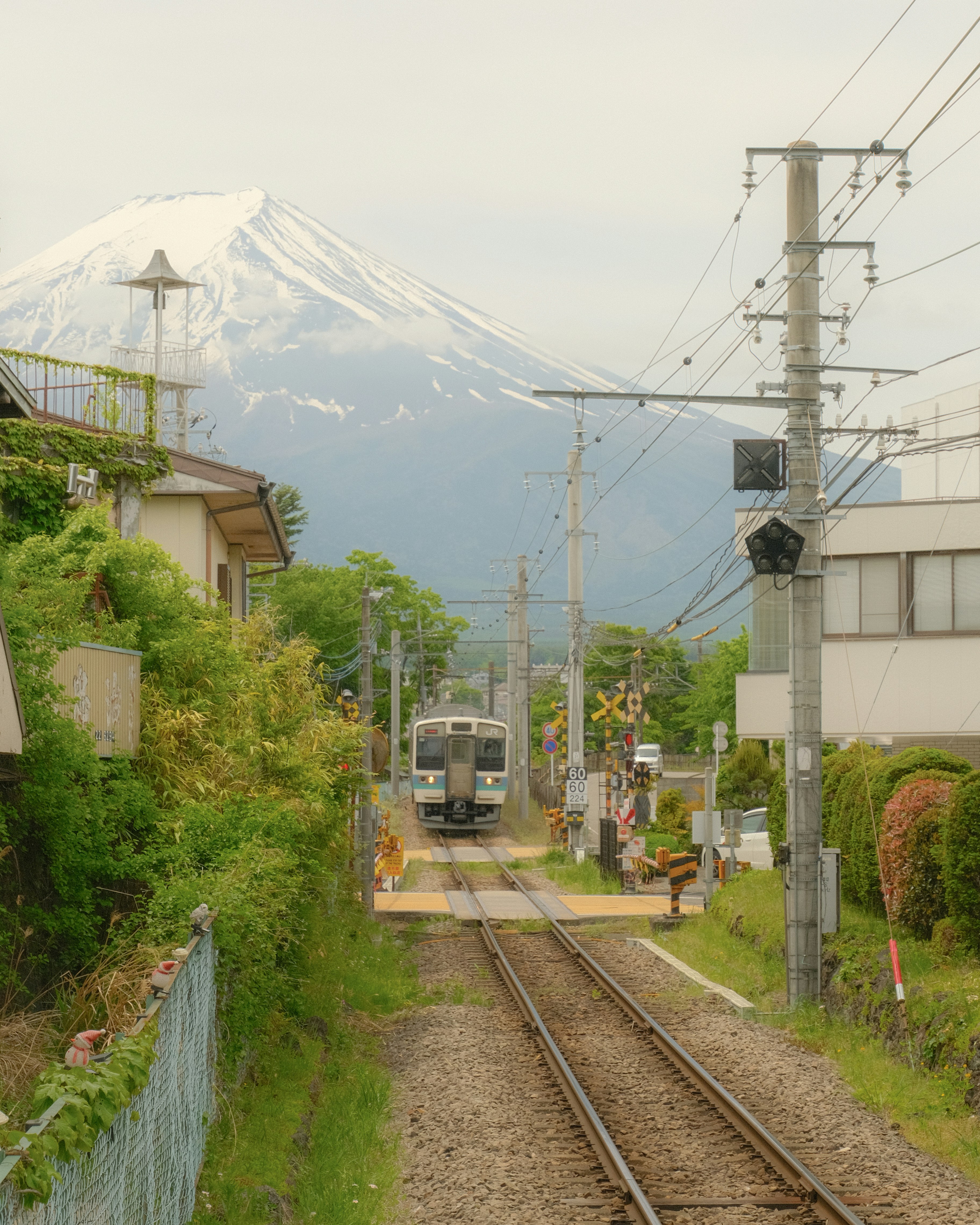 Train tracks lead to mount fuji under cloudy skies.