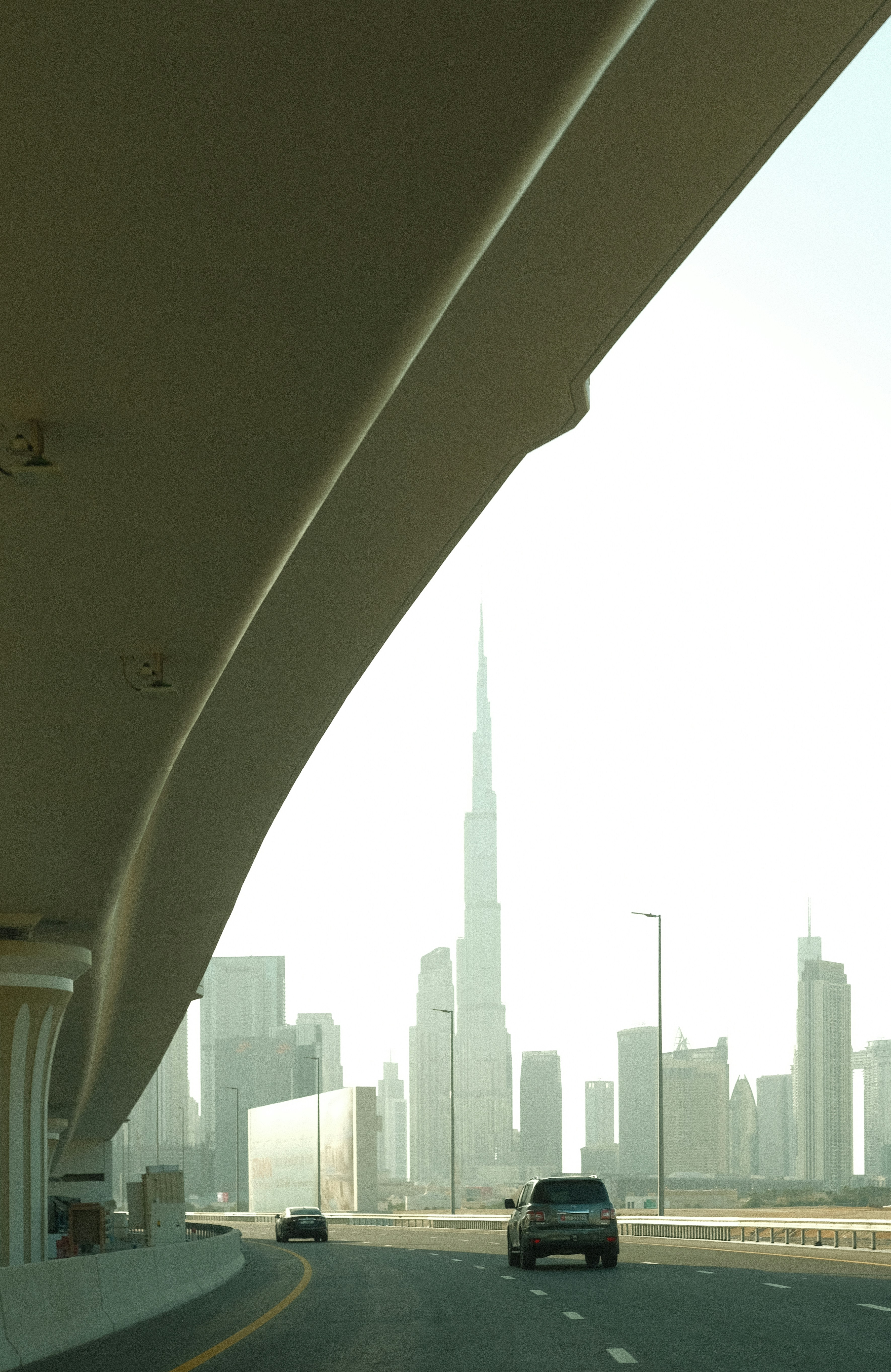 A highway view showcasing the iconic Burj Khalifa amidst a backdrop of Dubai's skyline, framed by an architectural overhang.