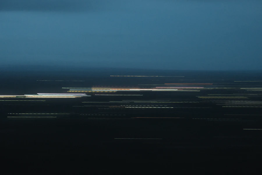 Long-exposure-style streaks of city lights stretch across a dark horizon under a deep blue evening sky.