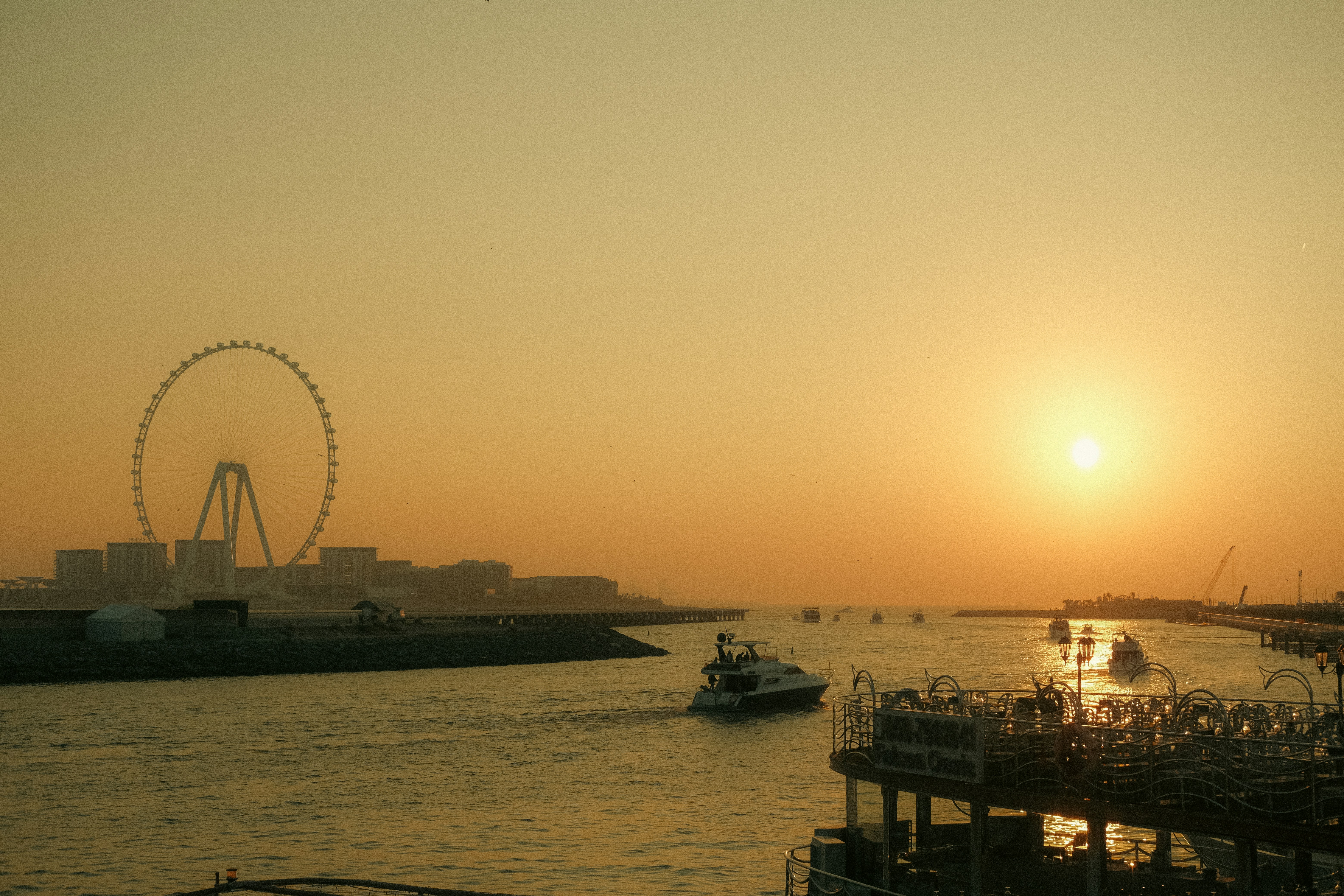Ferris wheel and boats on water at sunset