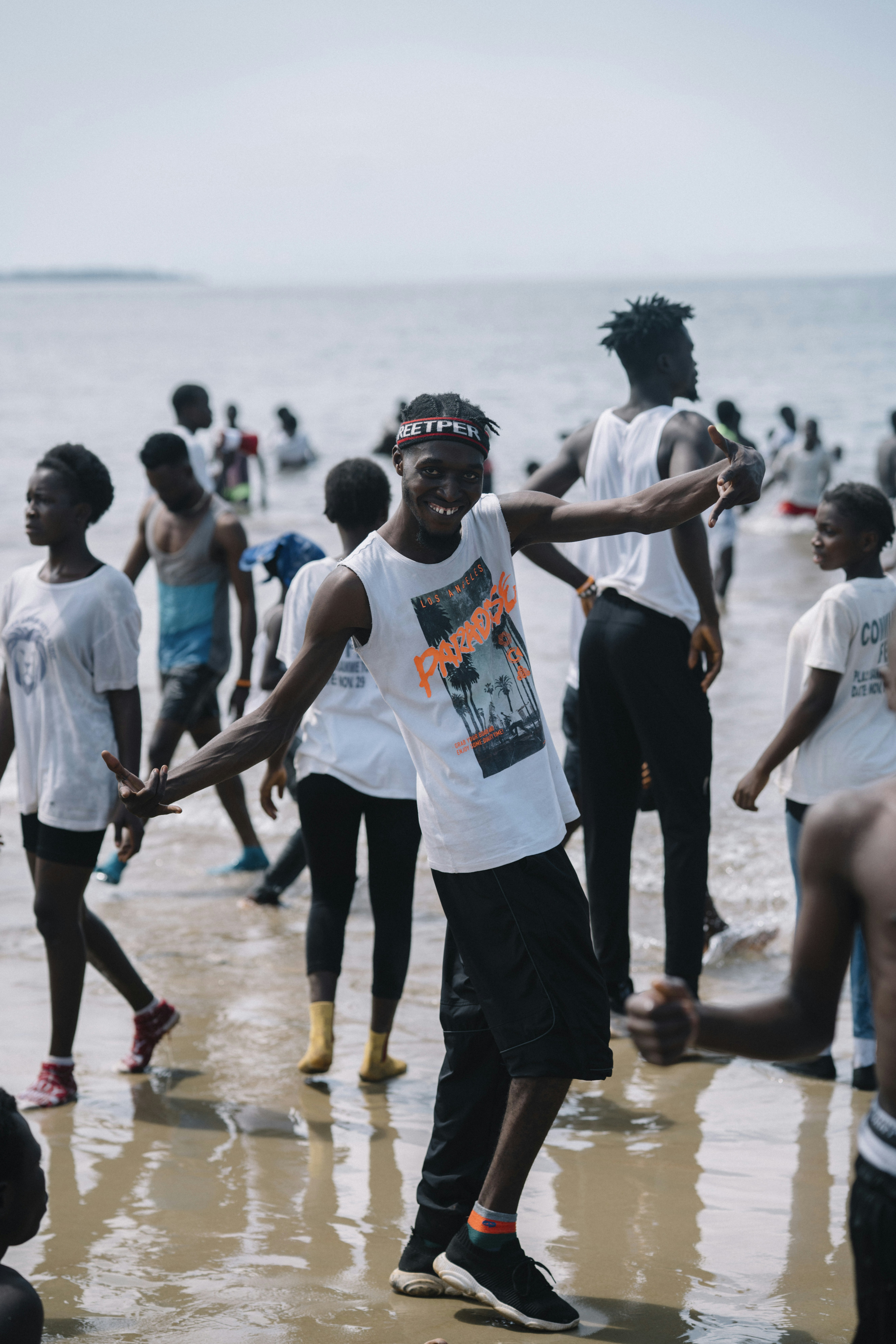 A group of young people enjoying a sunny day at the beach, with one individual playfully posing in the foreground. Their vibrant attire and lively expressions capture the essence of summer fun.