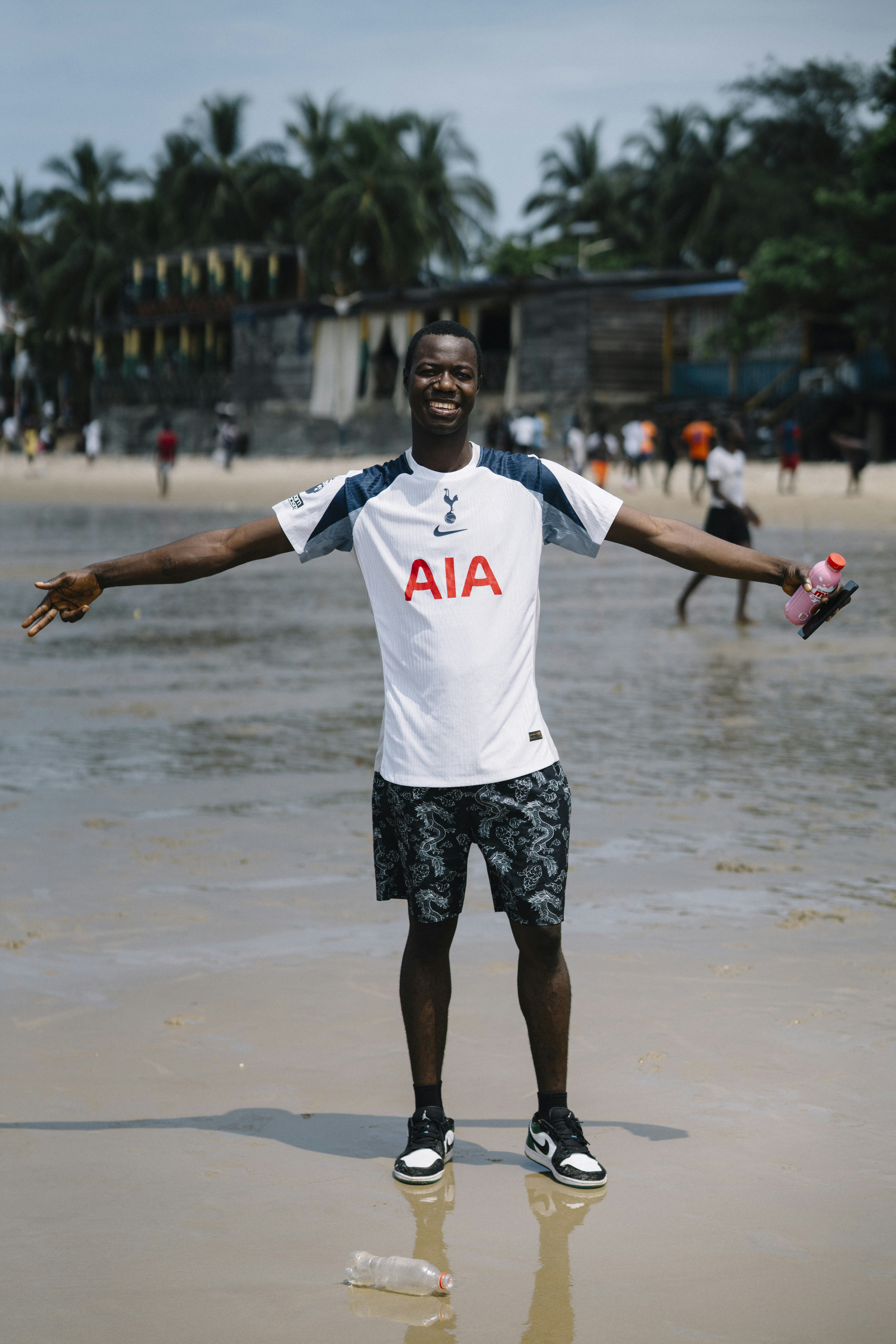 A smiling man in a soccer jersey on a beach.