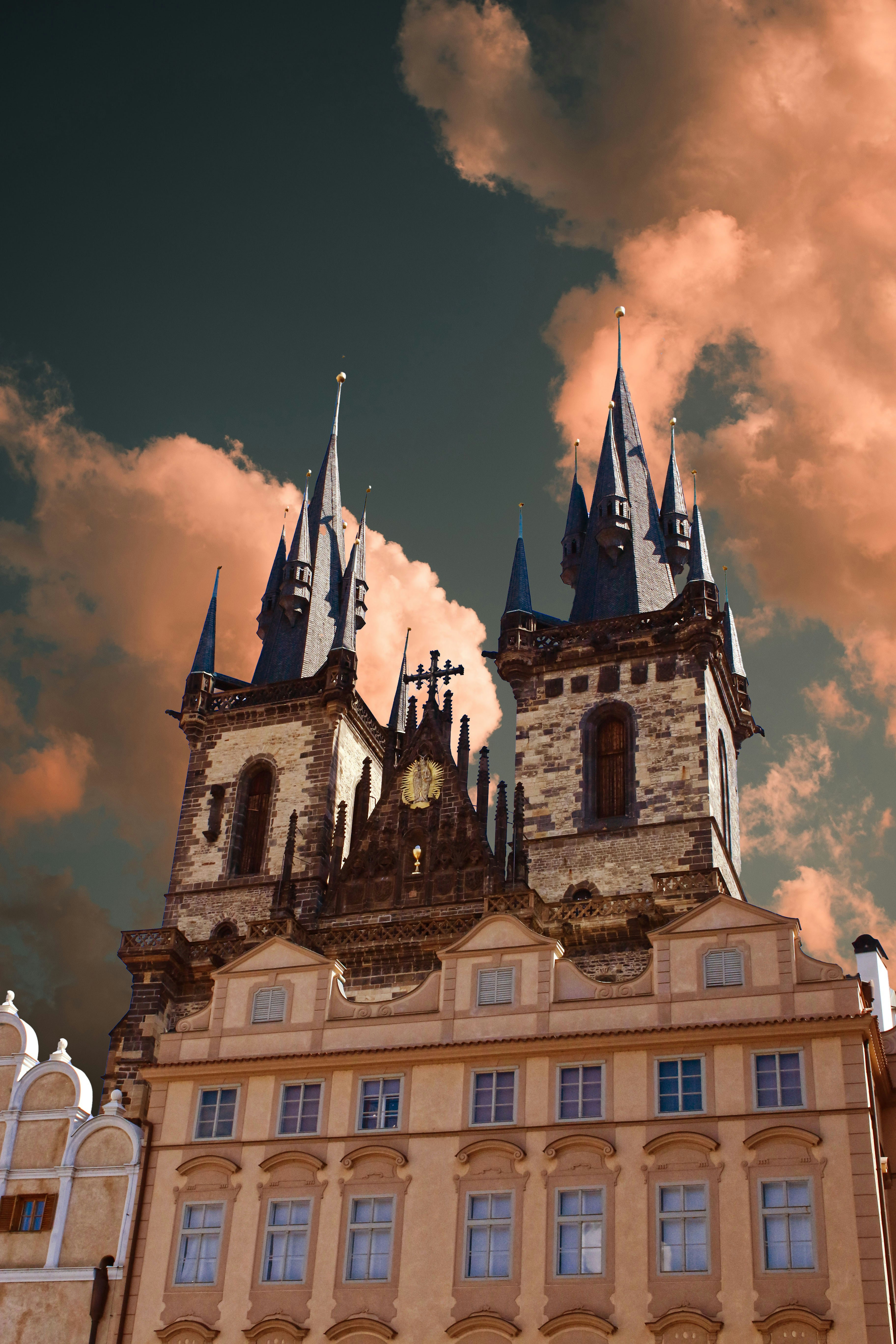 Historic towers of a Gothic building rise majestically under a dramatic sky, showcasing intricate architectural details. 