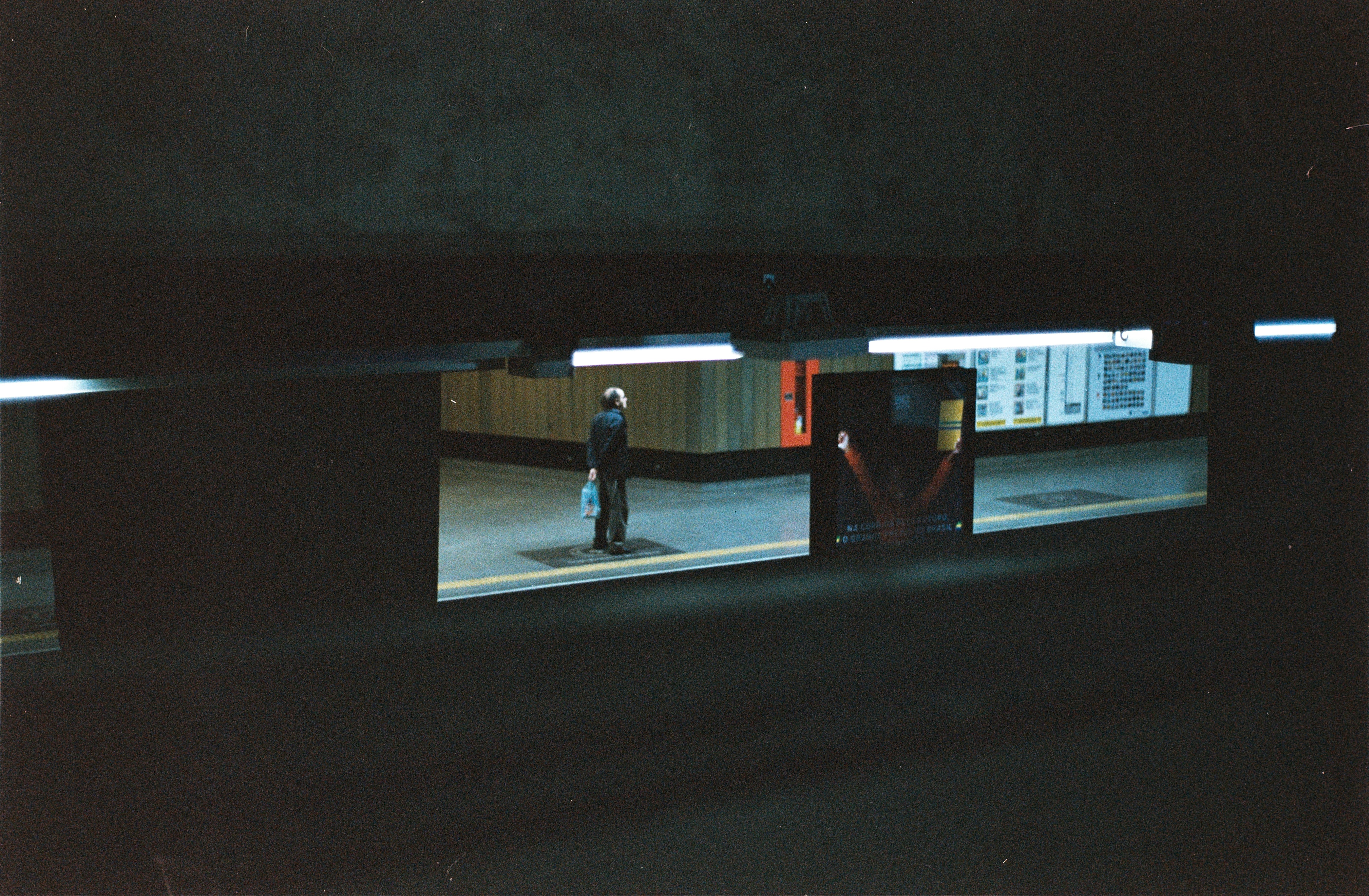 A man expecting a train; the platform is lit by blueish fluorescent lights and the photo feels like an Edward Hopper painting | A lone figure stands on a dark subway platform.