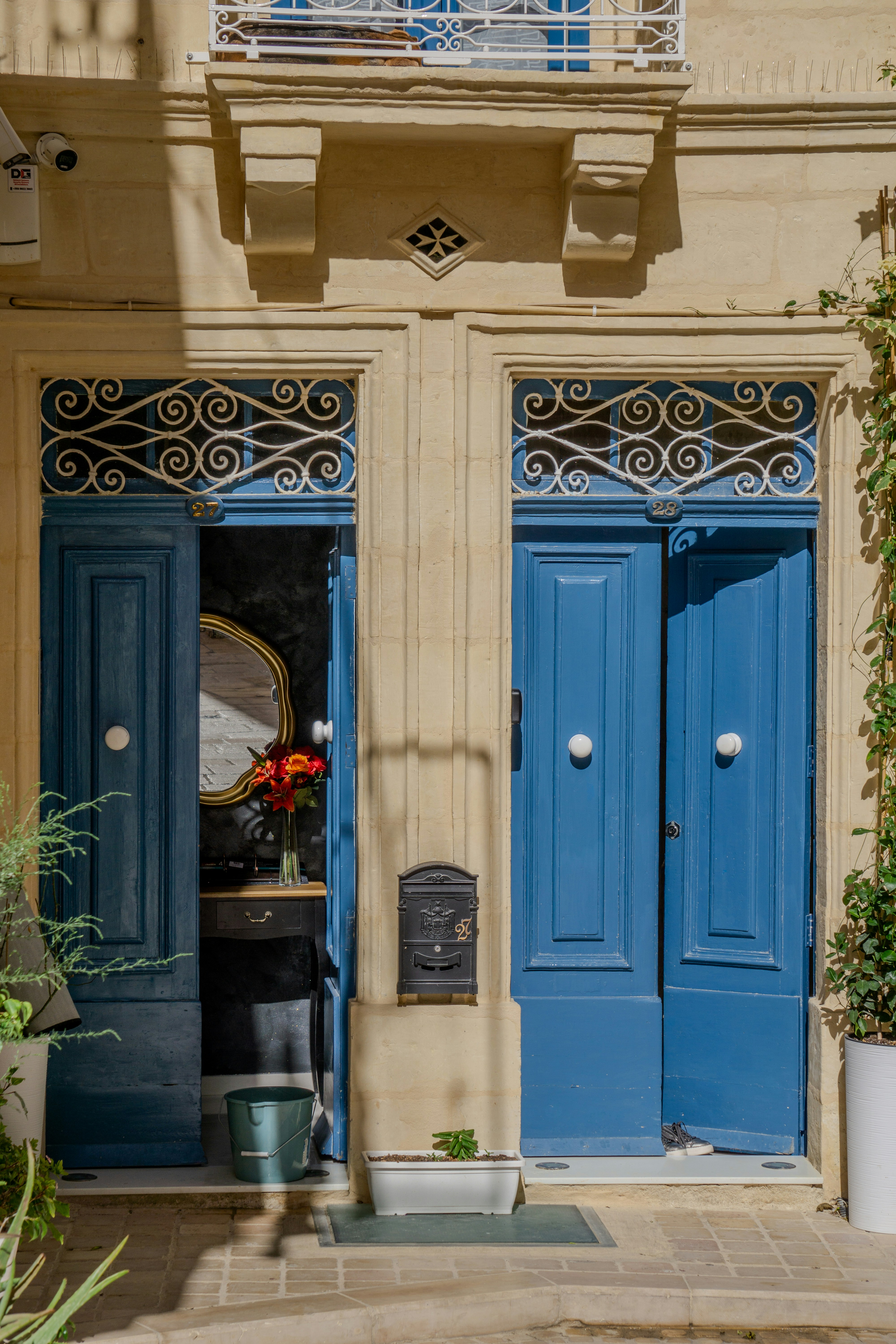Two blue doors, one open revealing a mirror and flowers.