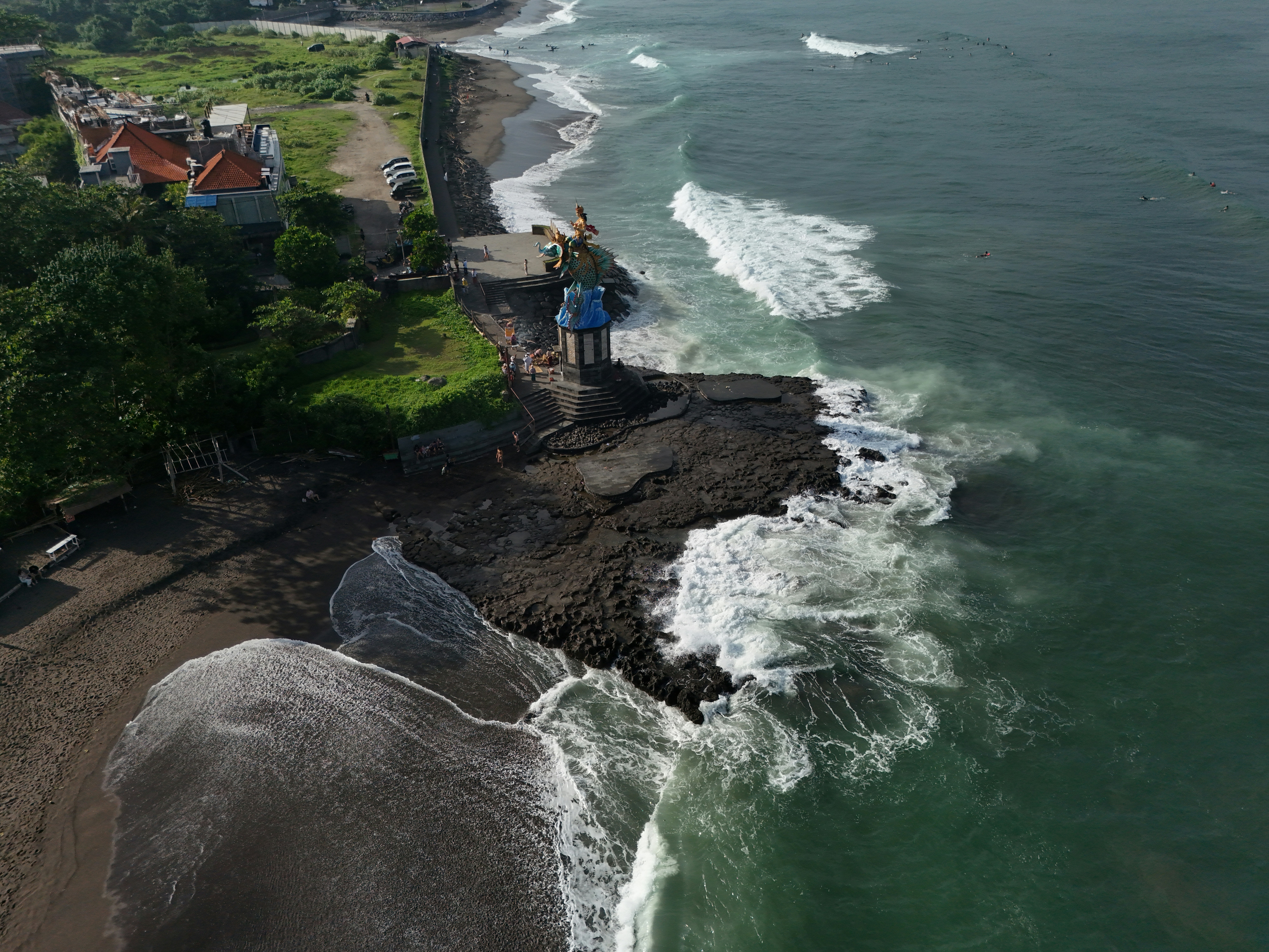 Waves crash on a rocky coastline with buildings nearby.