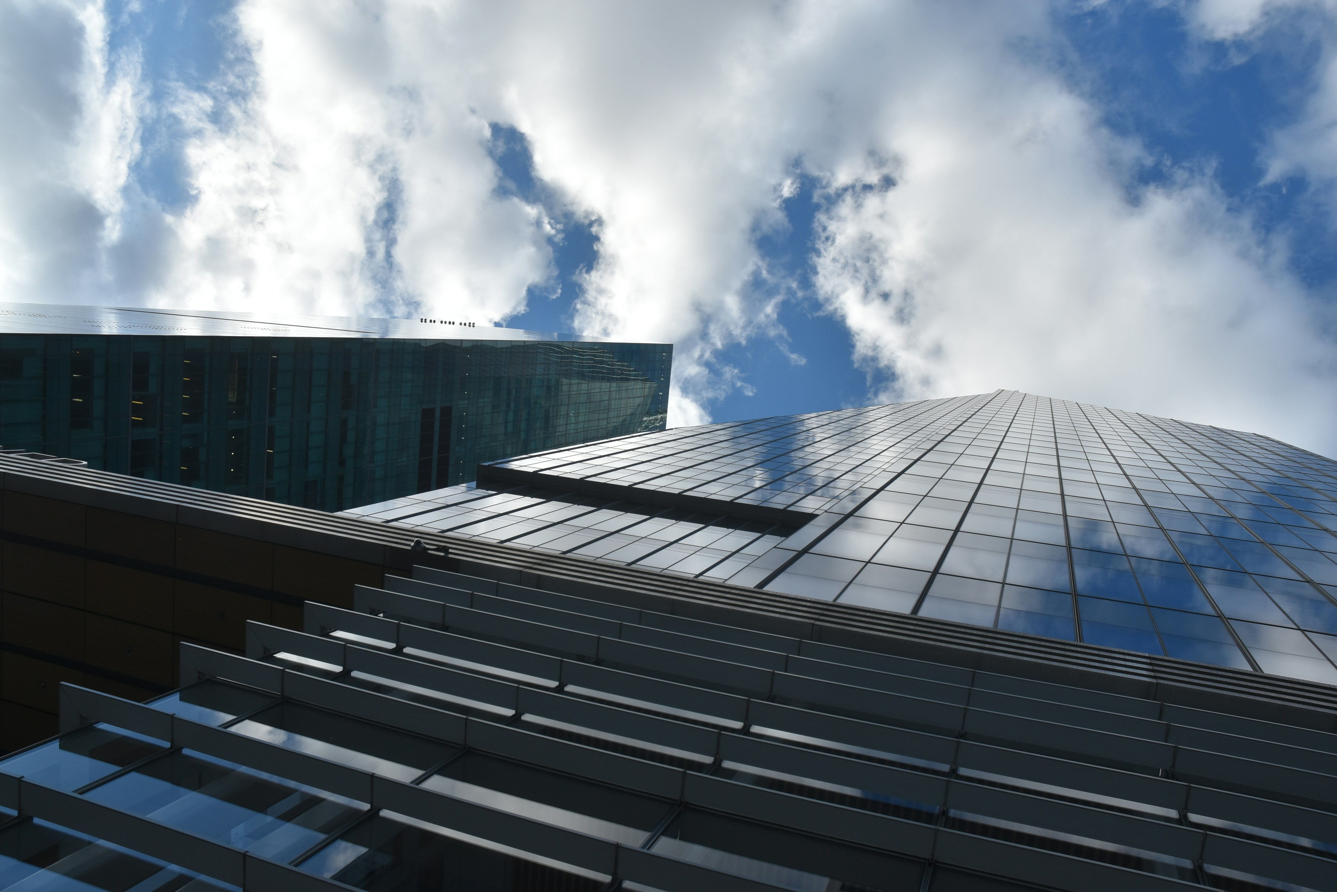 Glass skyscraper reflecting clouds against a bright blue sky, showcasing modern architecture and urban design.