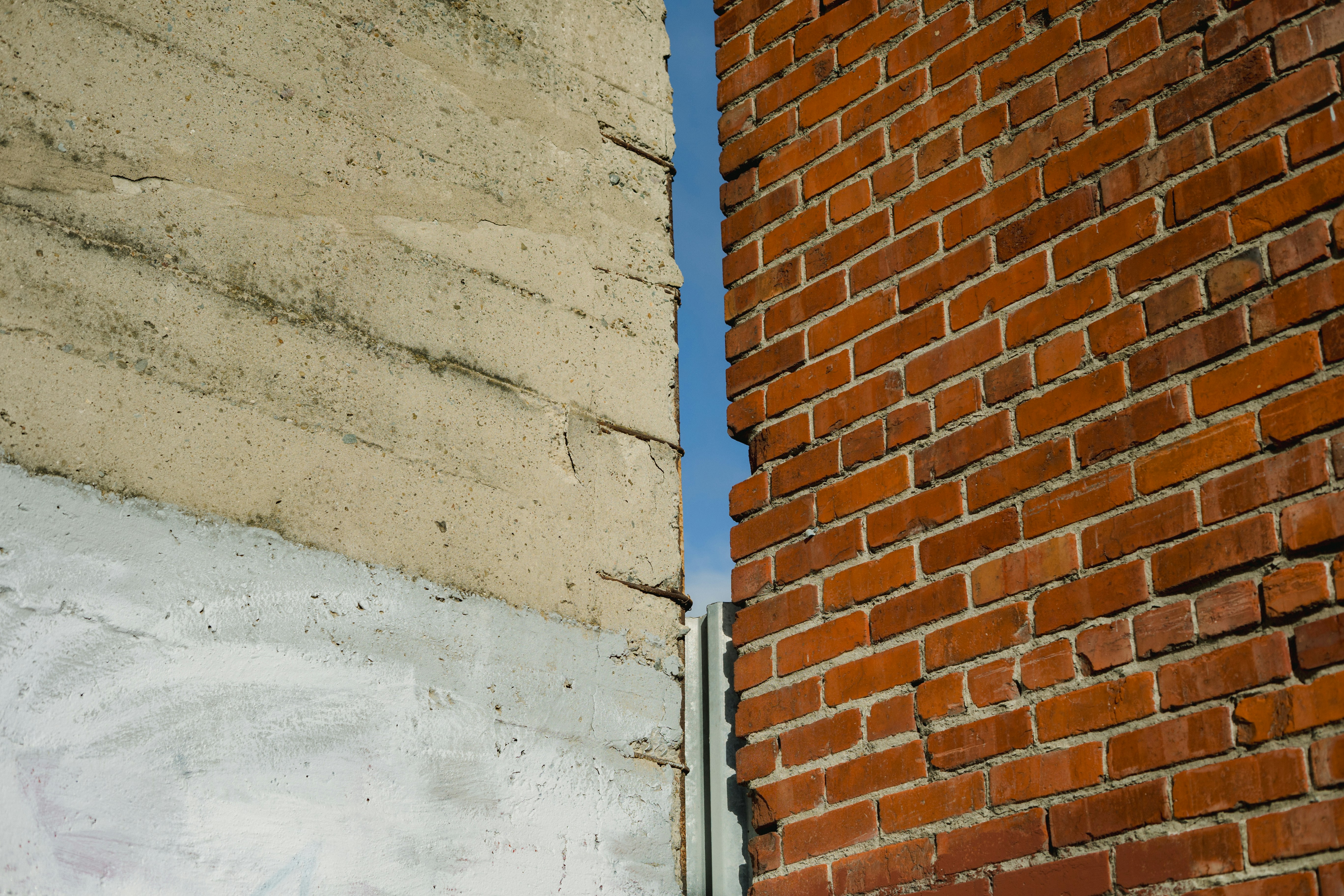 Two walls, one brick, one concrete, with sky visible