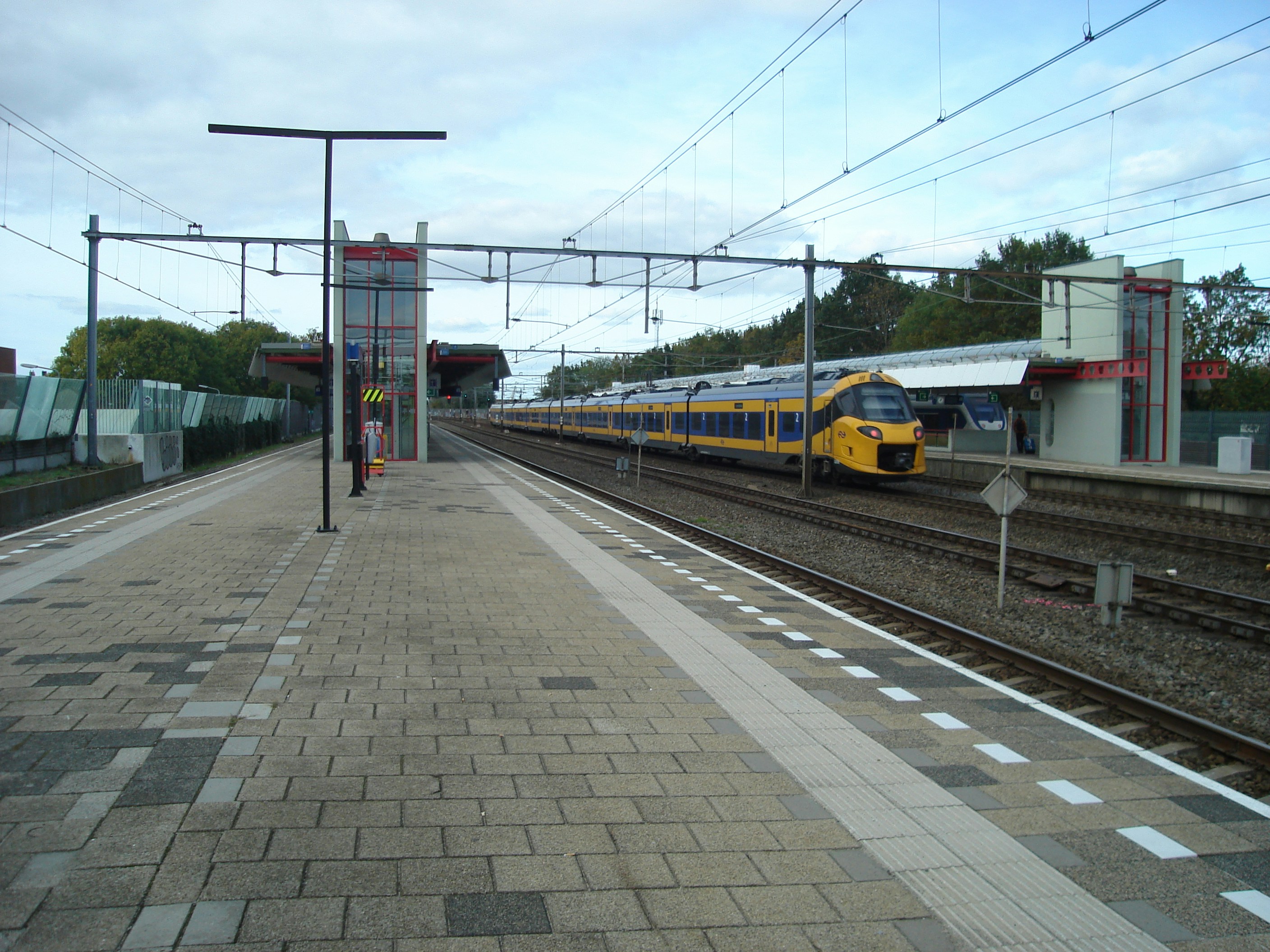 Weesp, Railwaystation | A yellow train approaches a modern station platform.