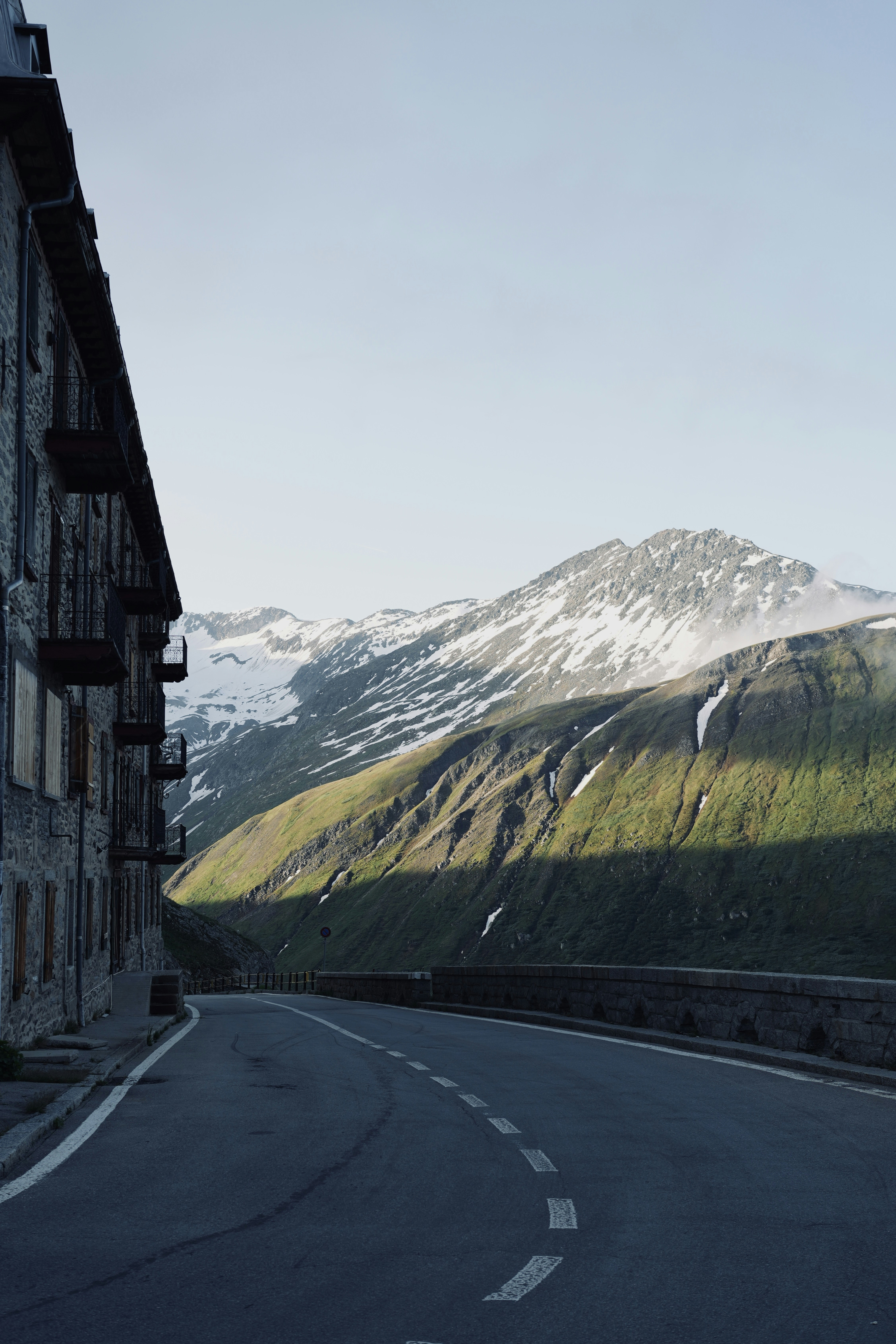 Mountain road next to stone building and snowy peaks.