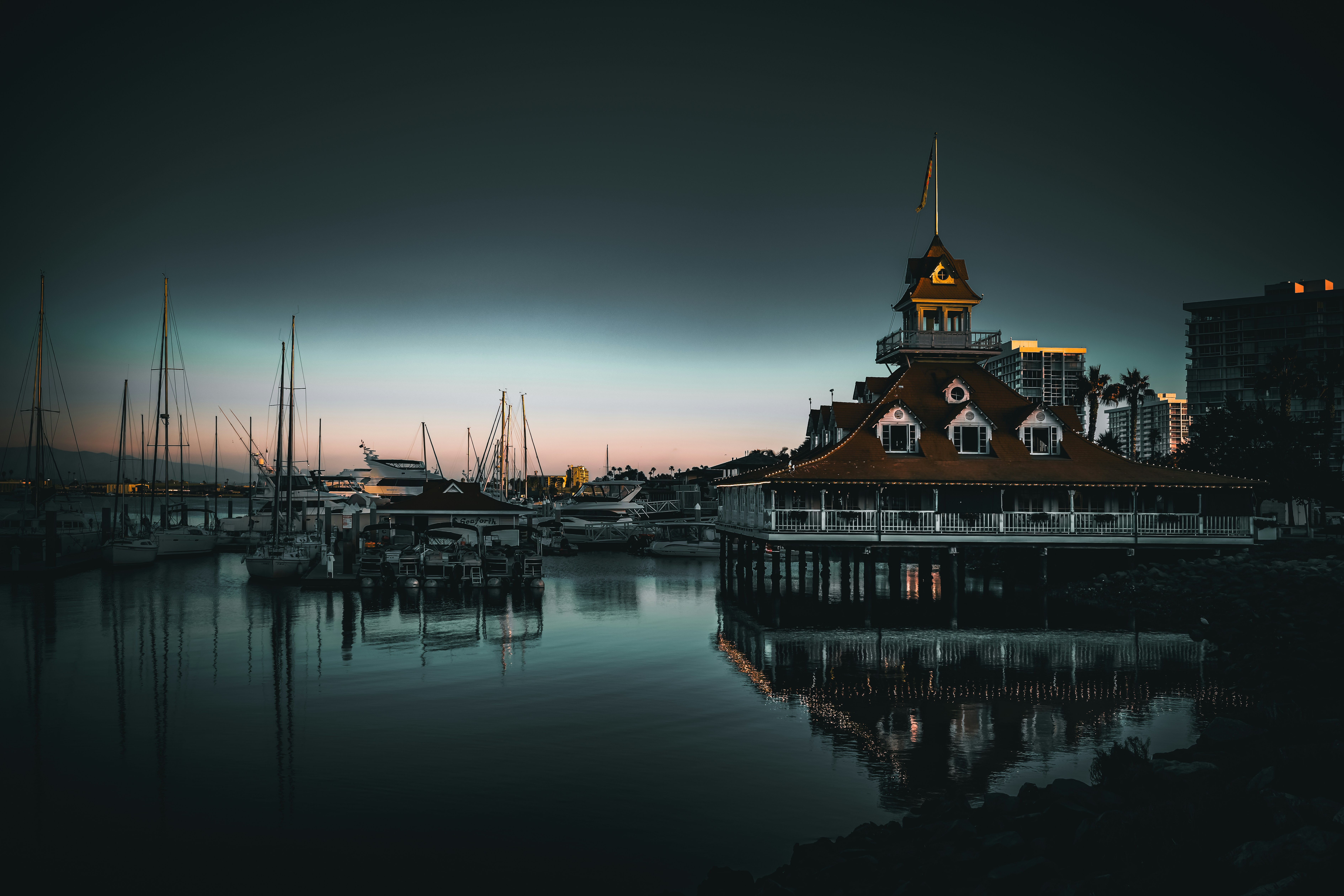 “Edge of Quiet” | Harbor building and sailboats at dusk with water reflection
