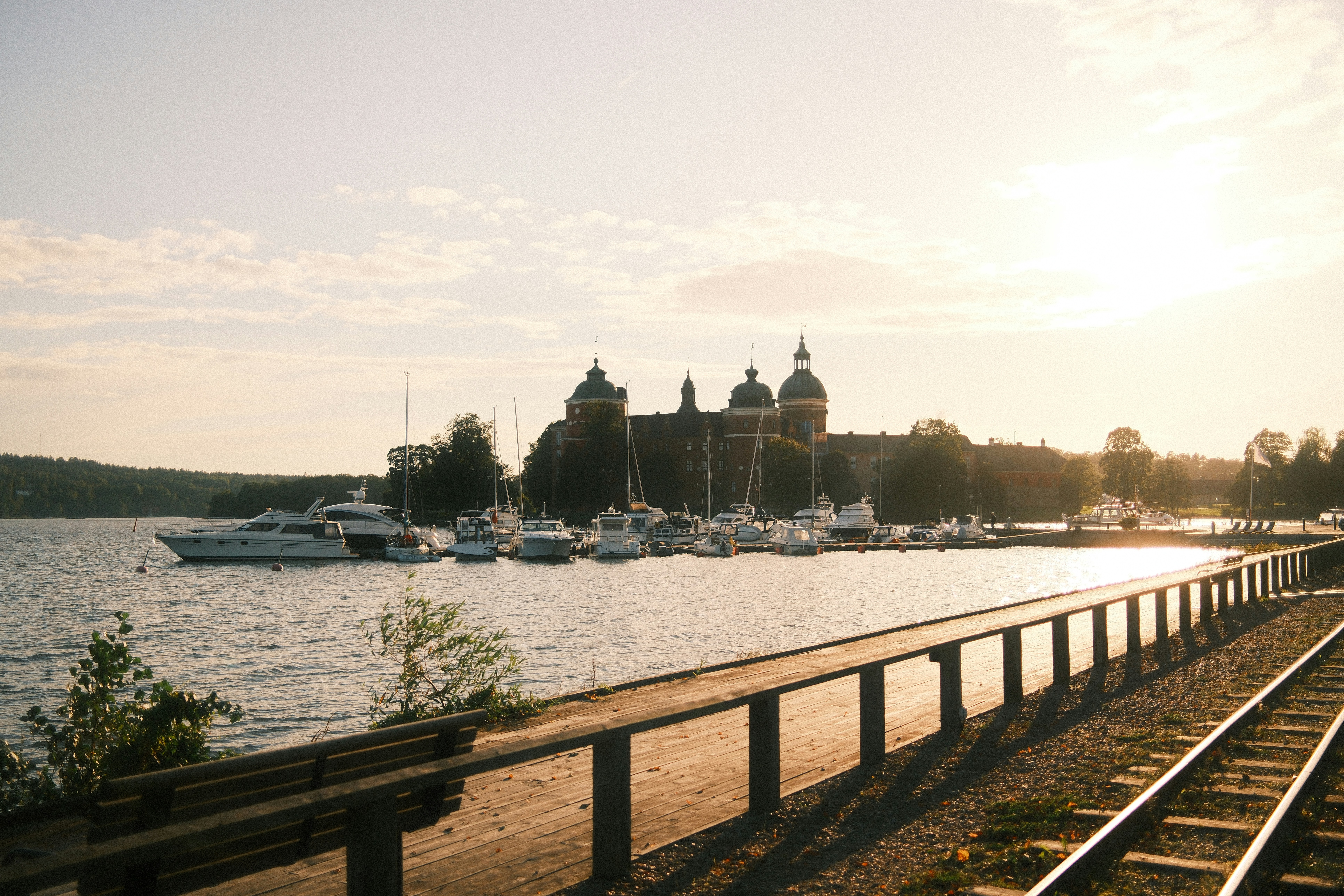 Castle by a lake with boats and train tracks.