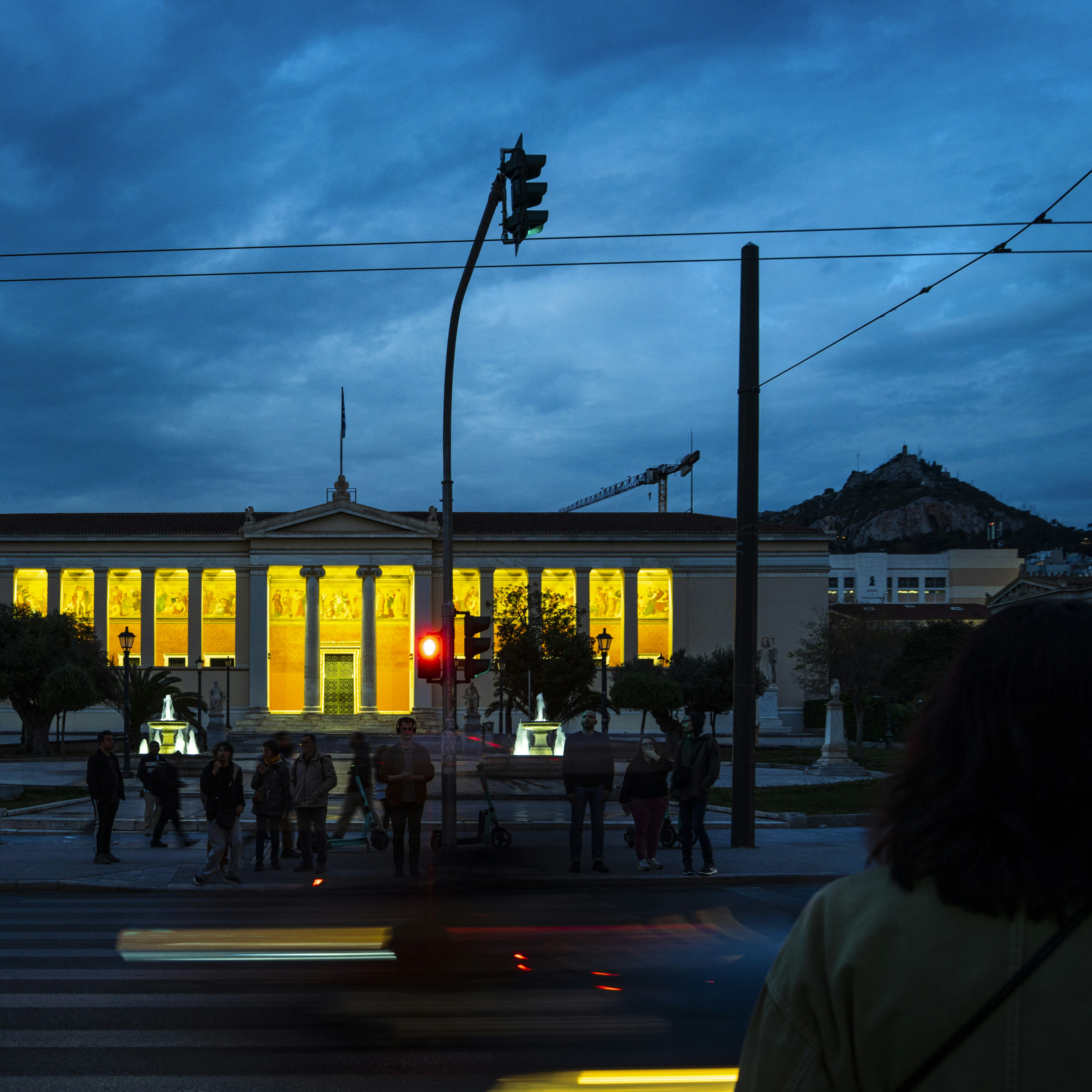 Building illuminated at night with people crossing street crossing street