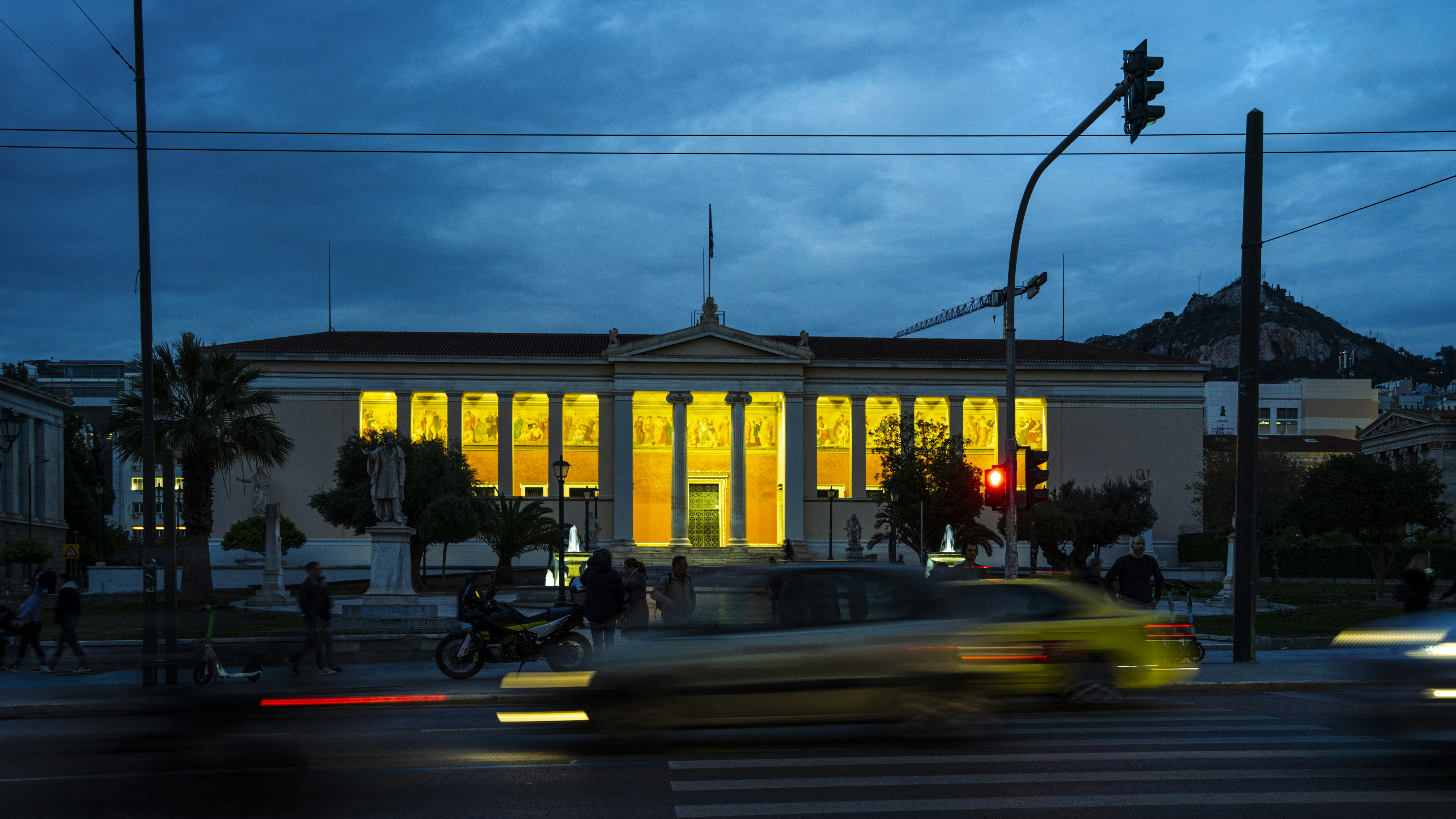 Historic building glowing warmly against a twilight sky, with bustling traffic in the foreground.