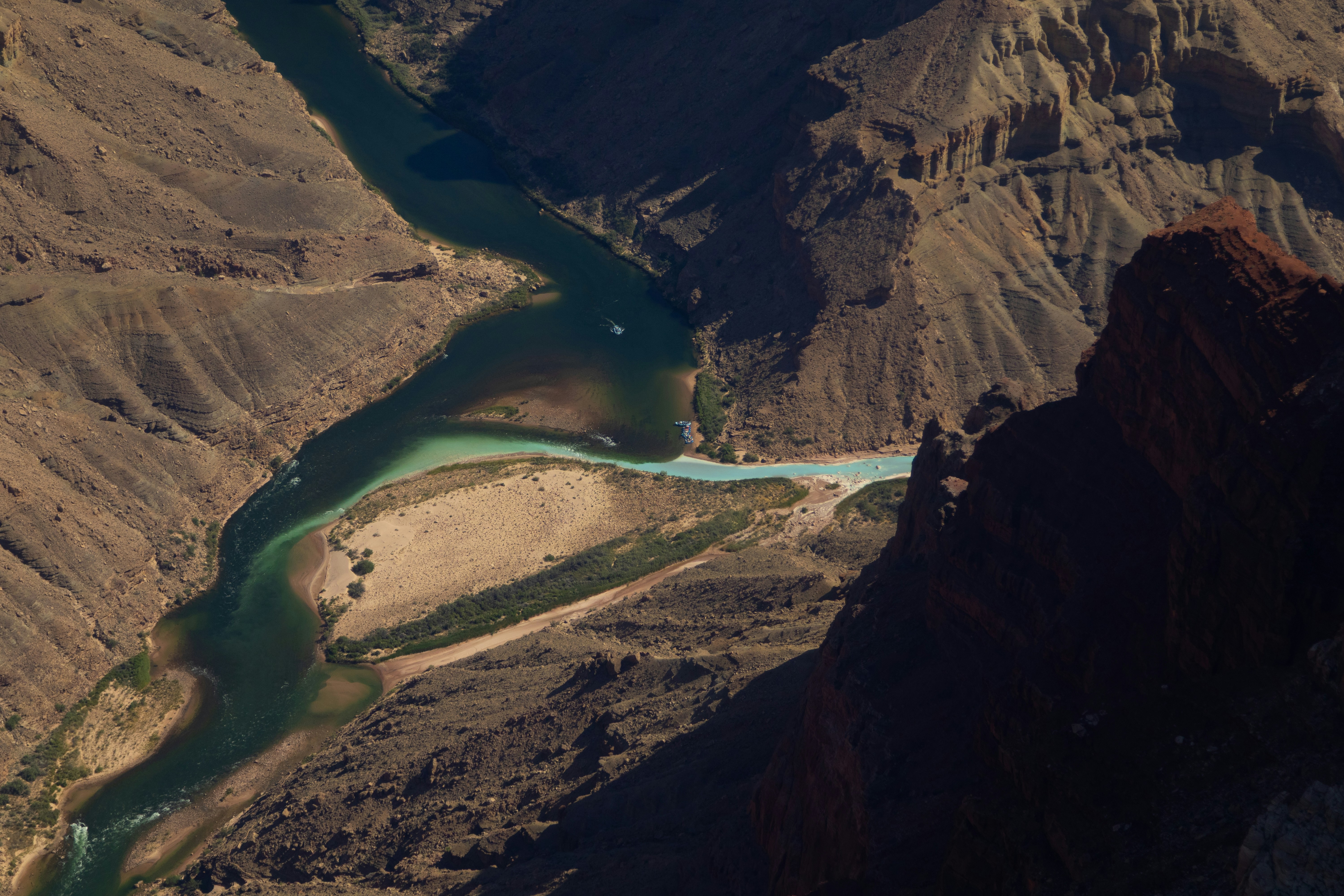 Aerial view of a serpentine river flowing through rugged canyon terrain, showcasing the stark contrast between the vibrant water and arid landscape.