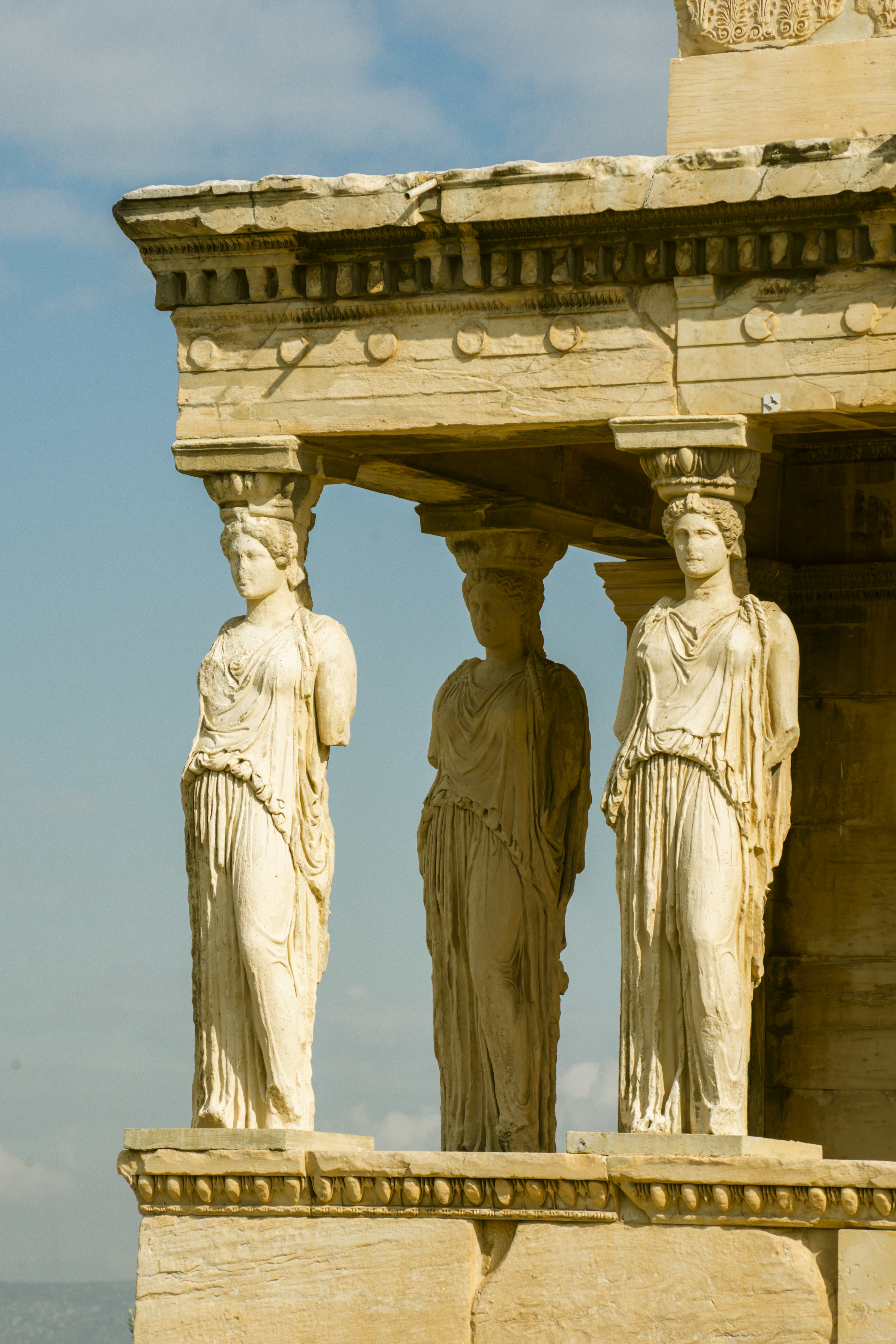 Sunlit Caryatid Trio Framing a Weathered Classical Frieze