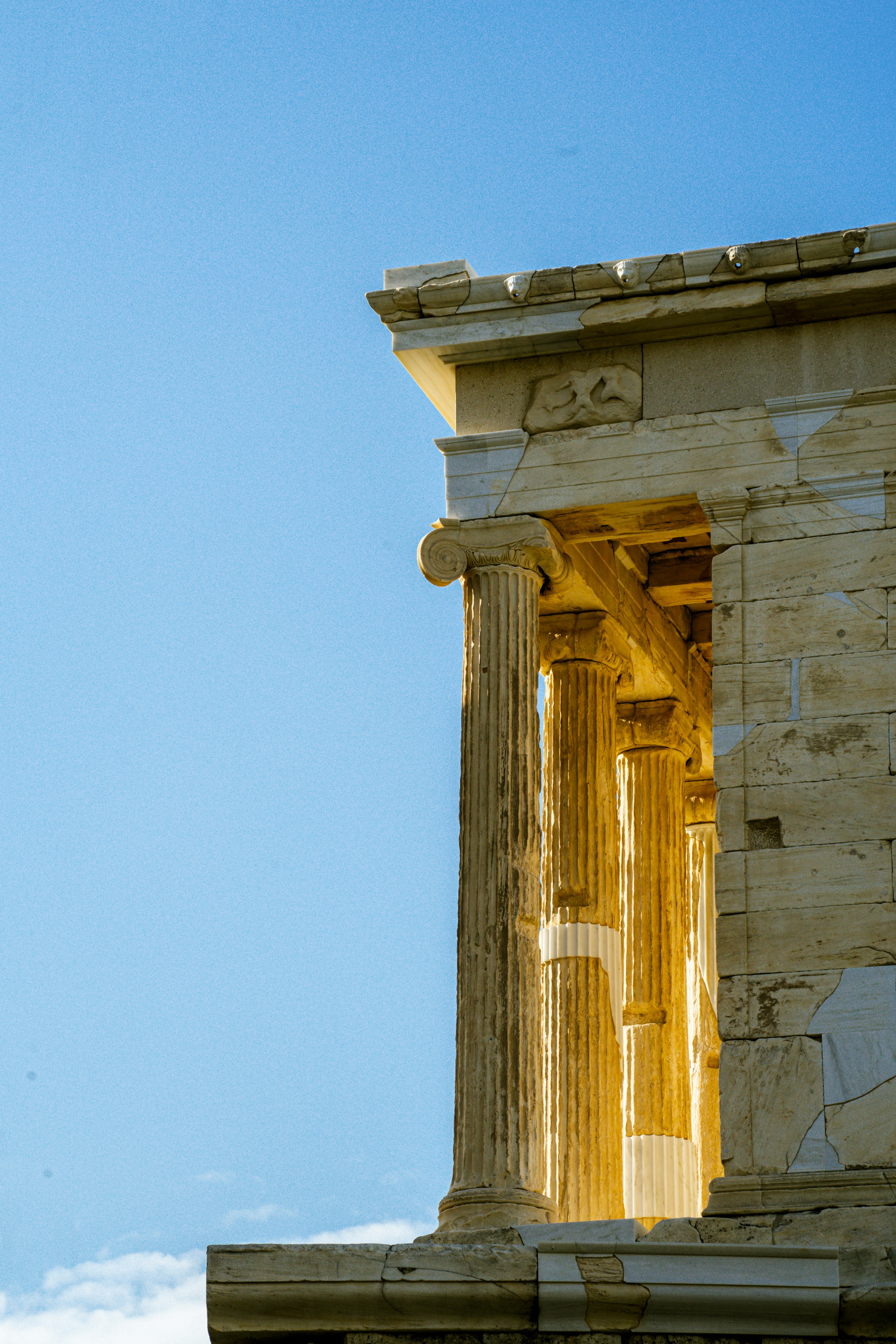 Ancient Greek temple columns illuminated by sunlight against a clear blue sky, showcasing intricate architectural details.