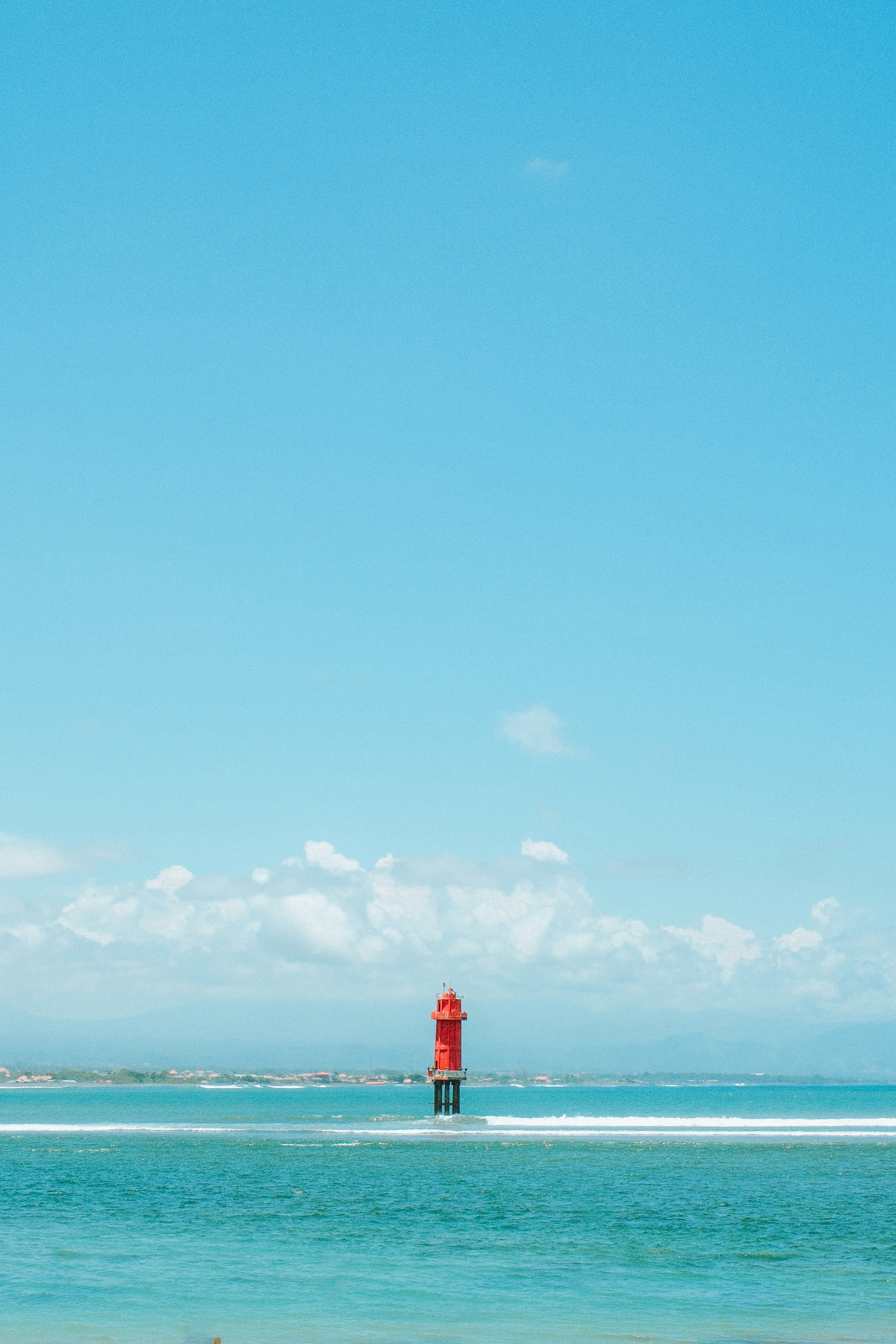 Red lighthouse standing in the ocean water.