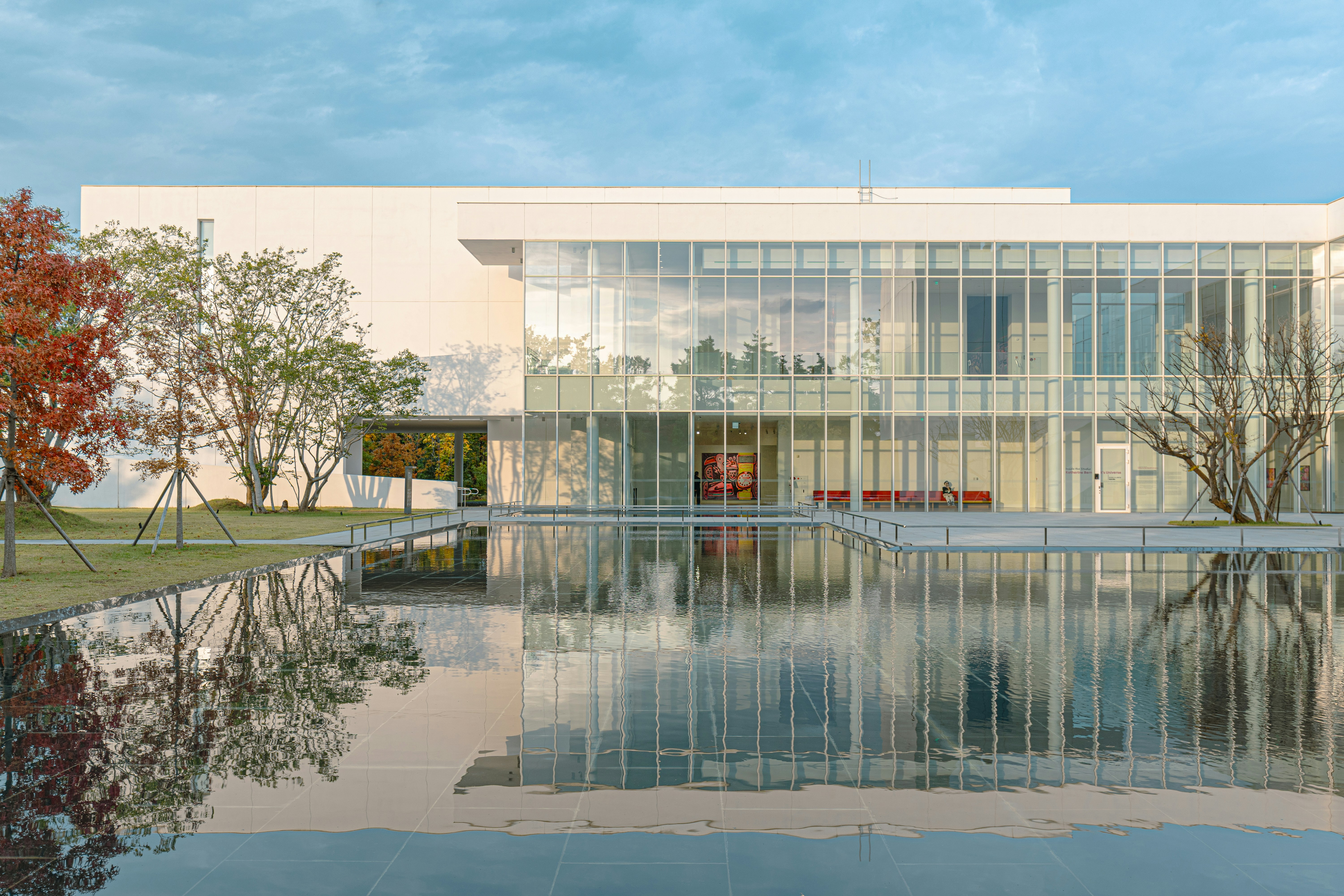 Contemporary architecture reflected in a tranquil pool, surrounded by lush greenery and autumn foliage.