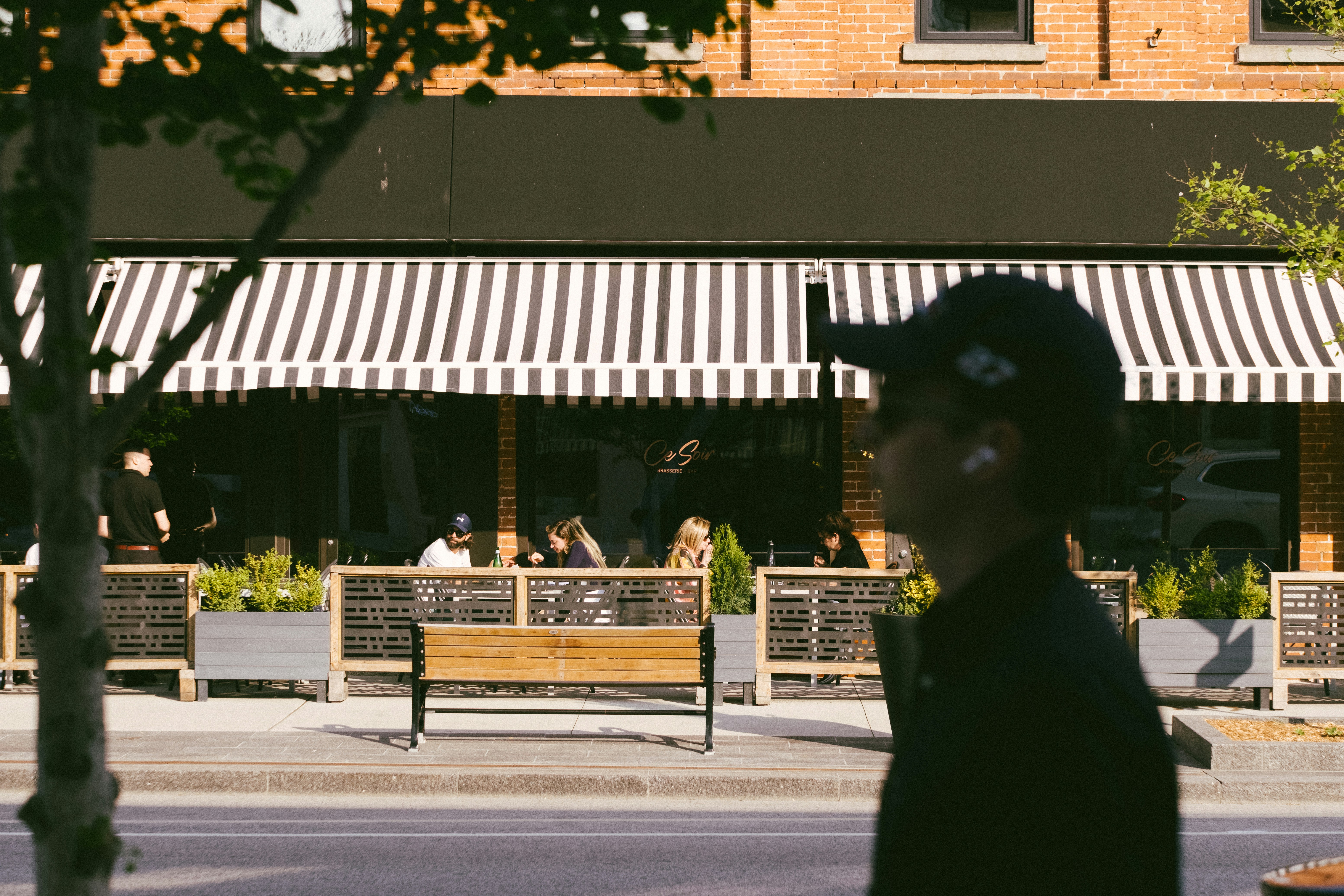 Person walks past outdoor cafe with striped awning.
