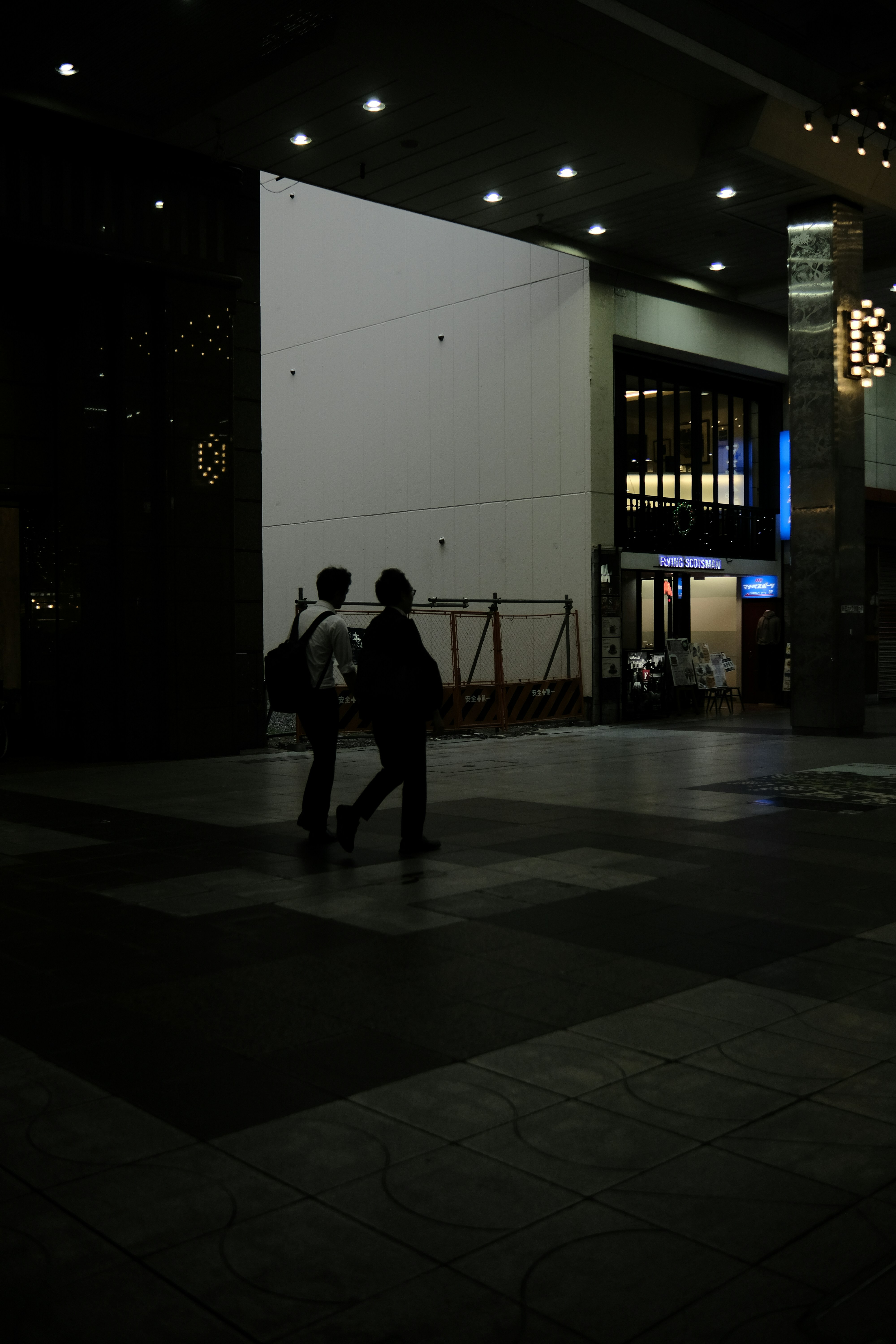 Two people walking in a dark urban area at night.