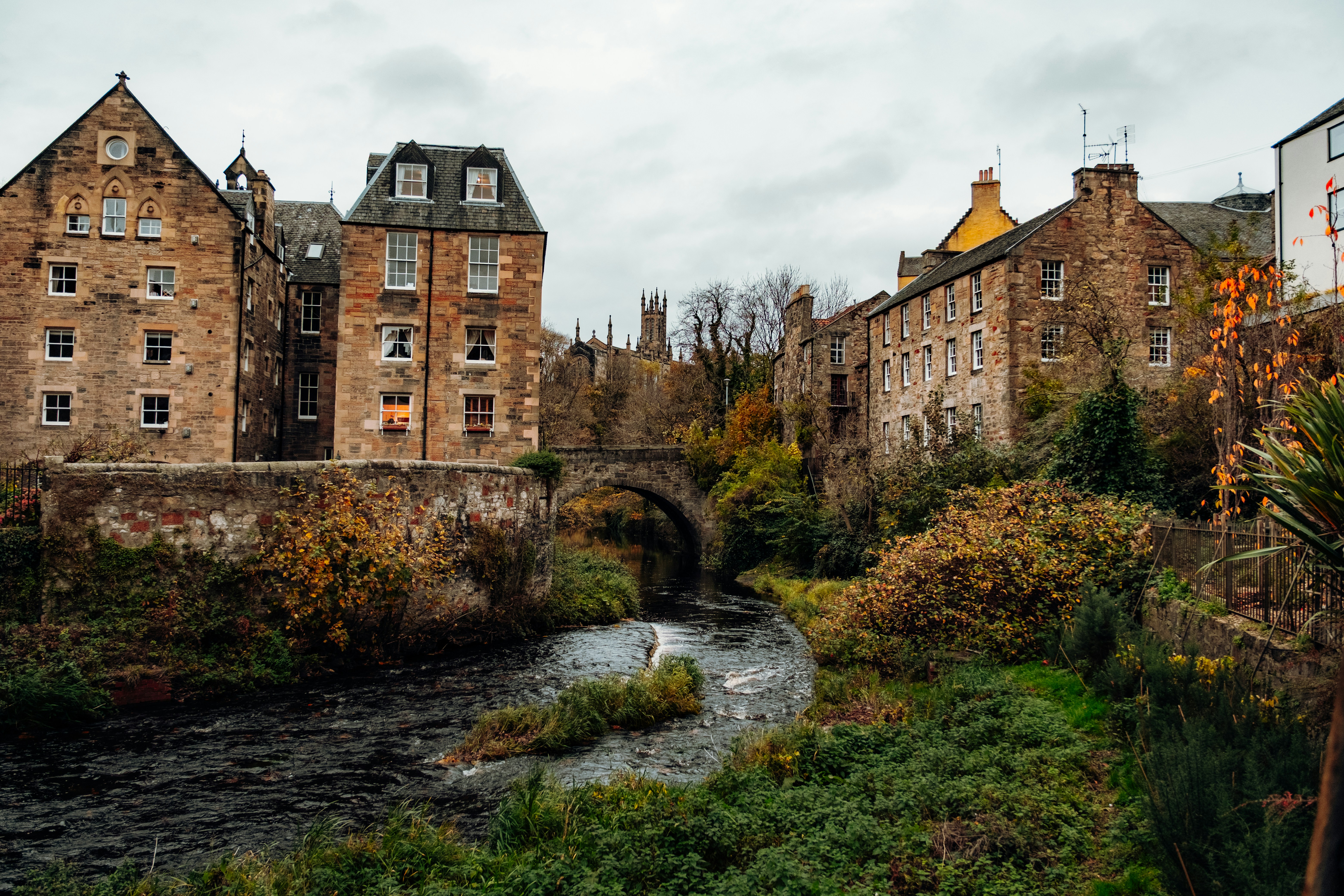 Stone buildings line a river with autumn foliage.