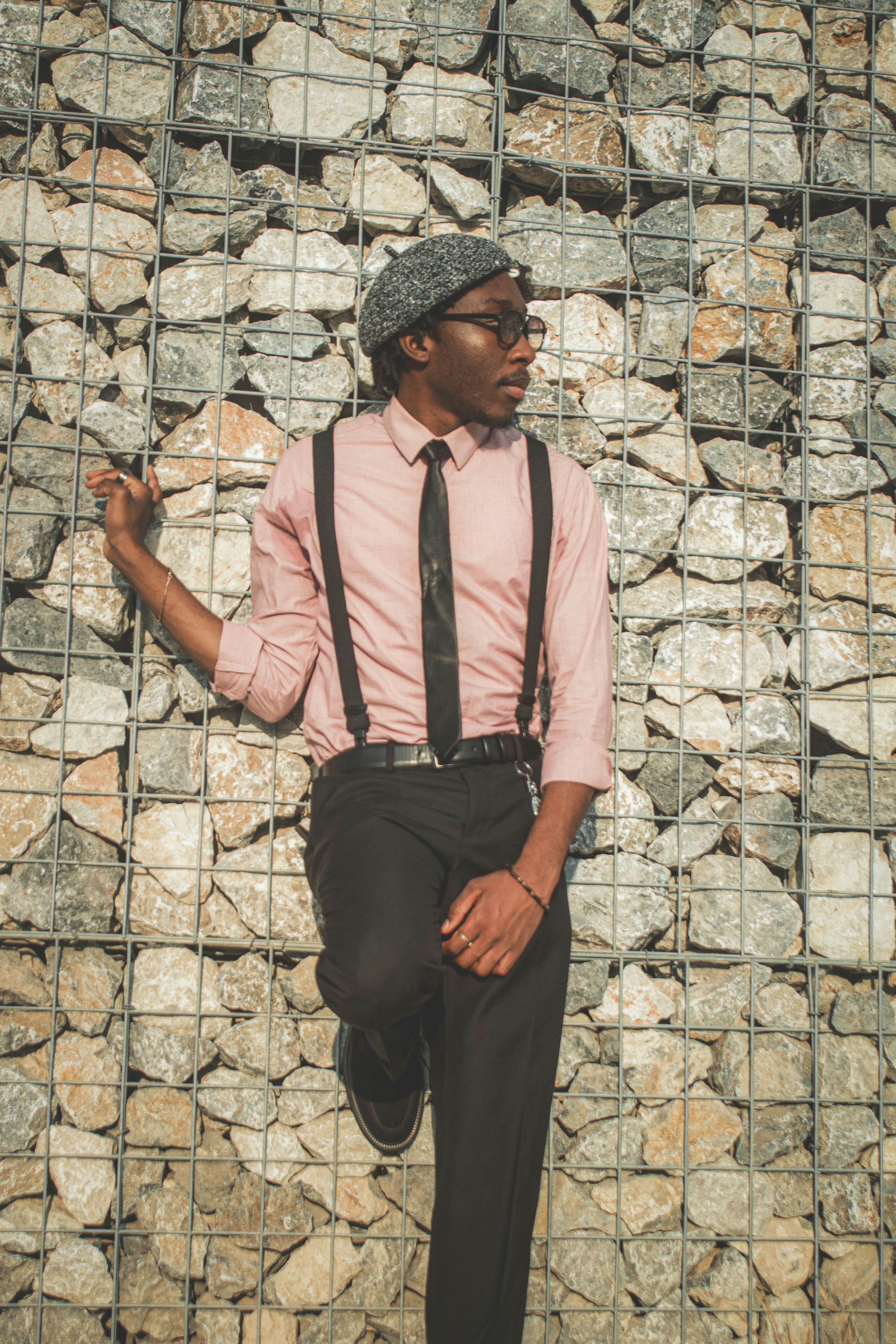 Man in vintage clothing leans against stone wall