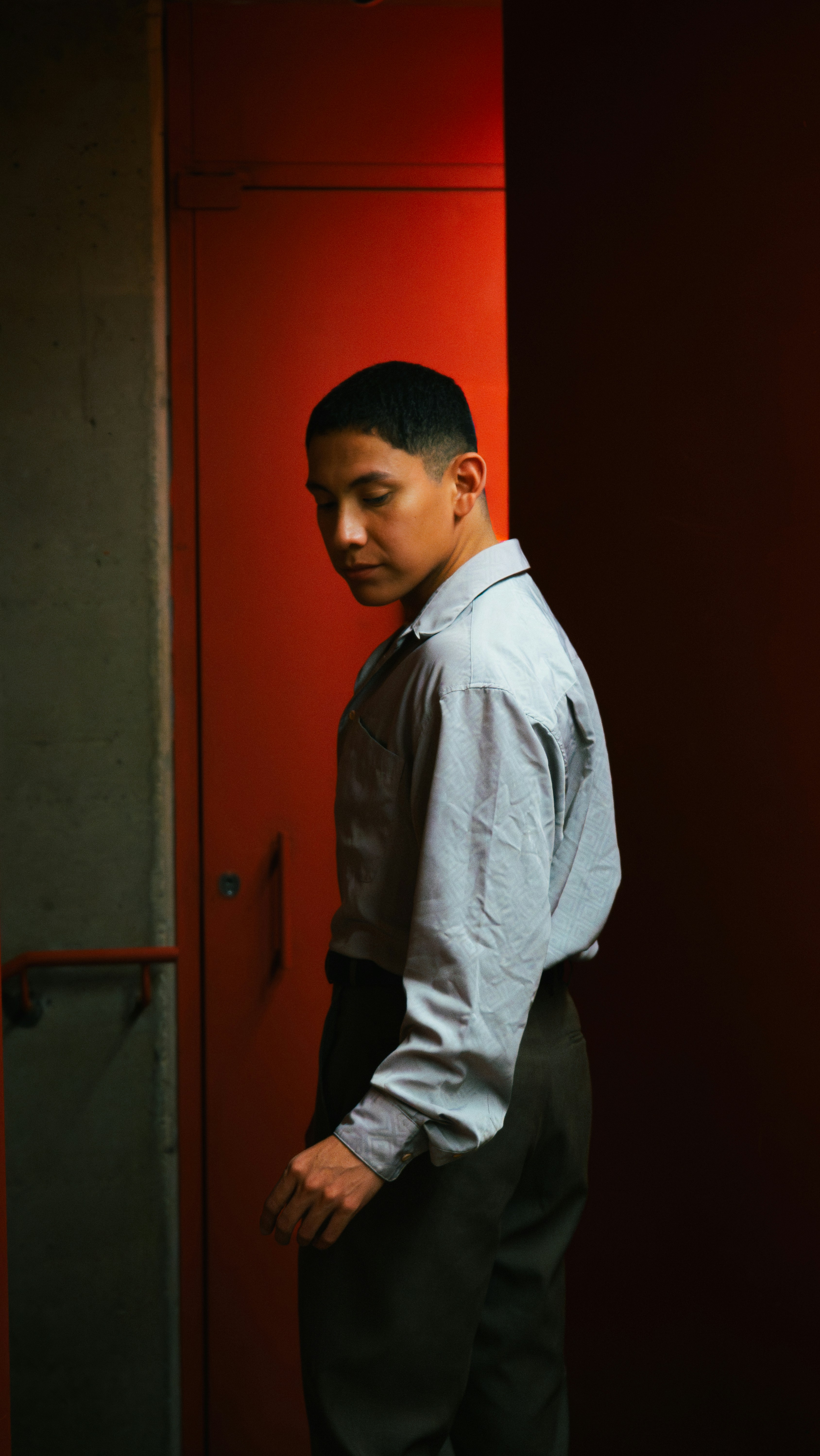 Man in collared shirt looking down against red wall