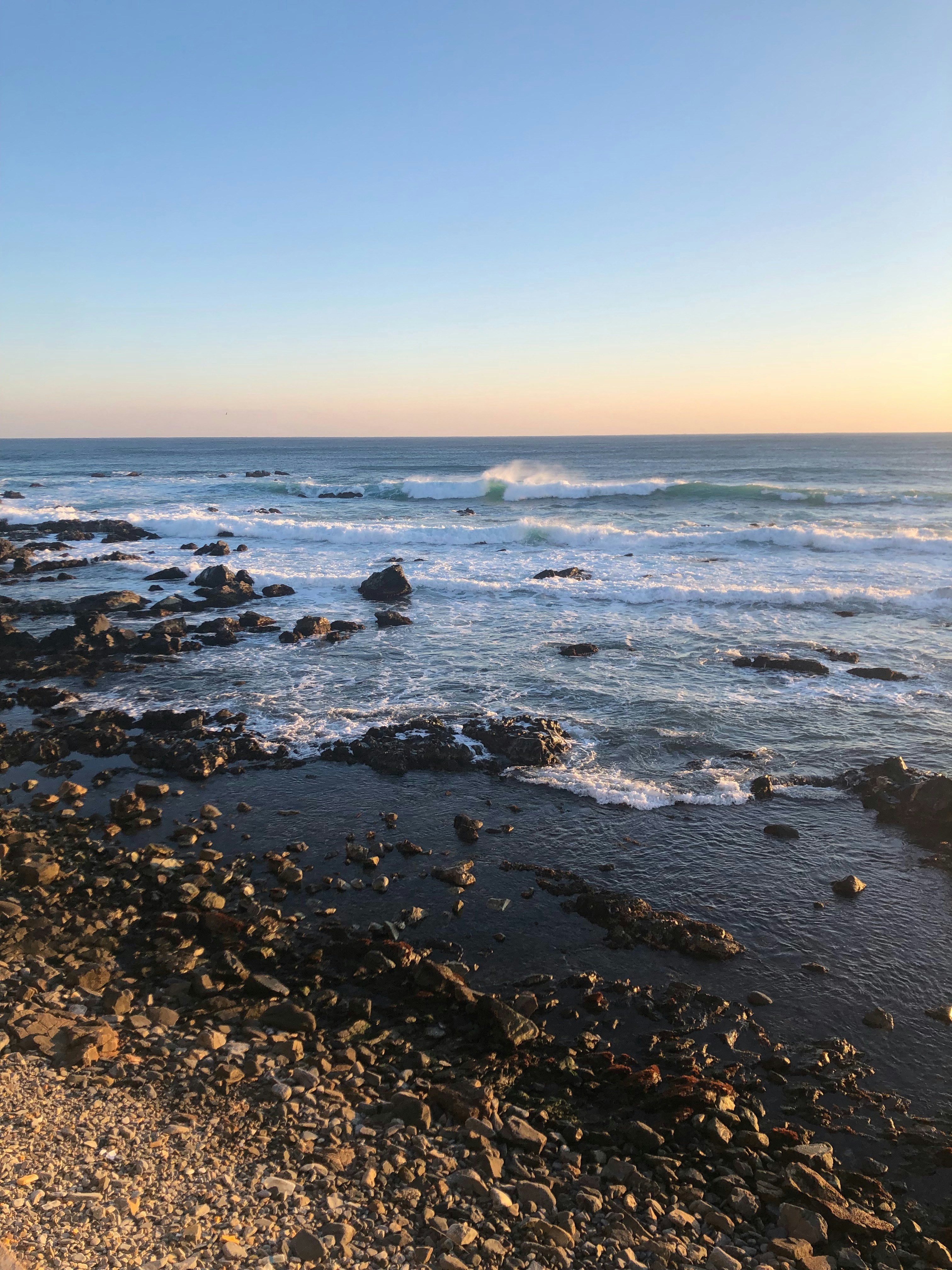 Waves gently lap against rocky shores under a pastel sky at sunset.