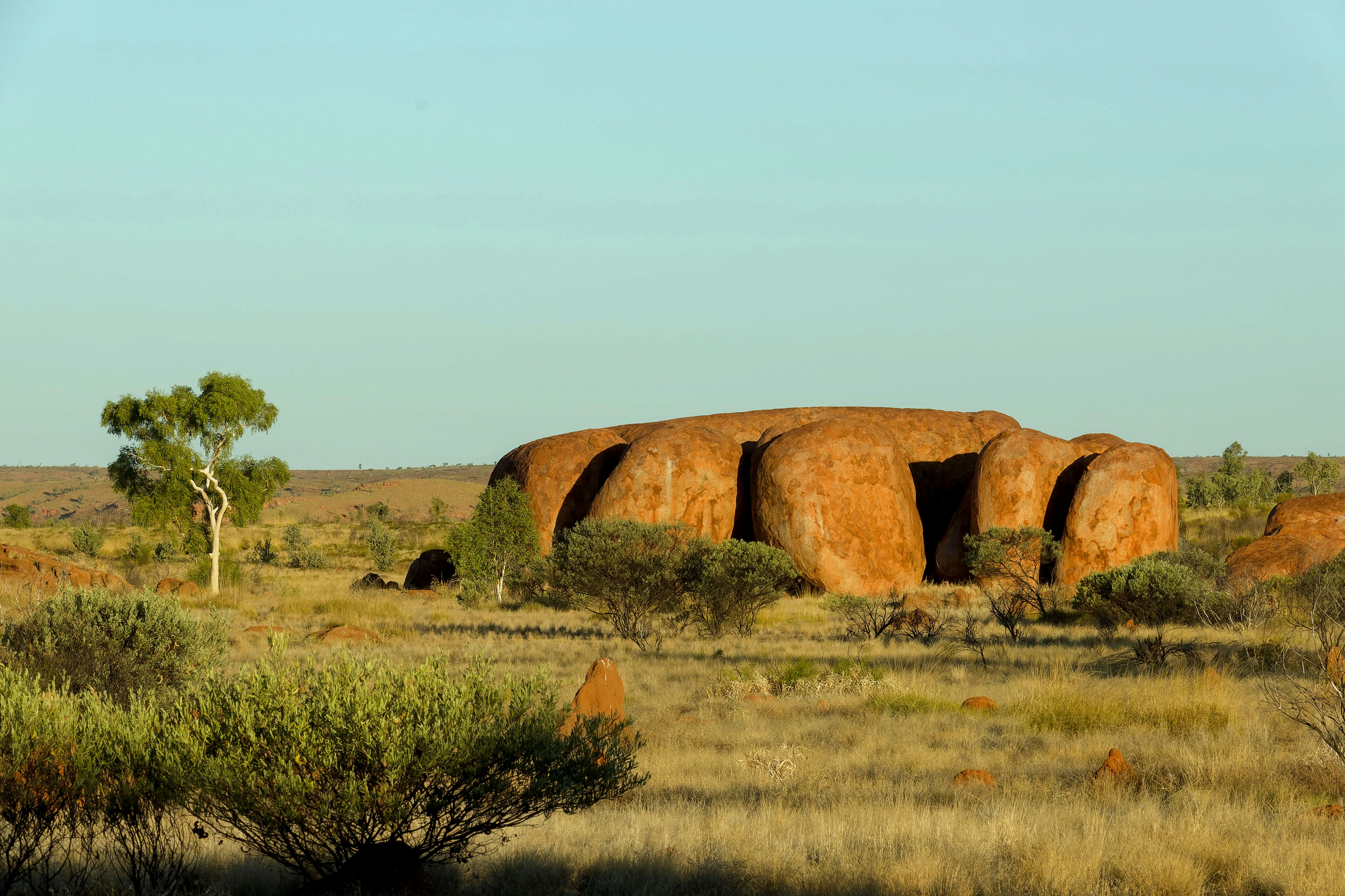 Large sandstone formations rise prominently in the arid landscape, surrounded by sparse vegetation and distant hills.