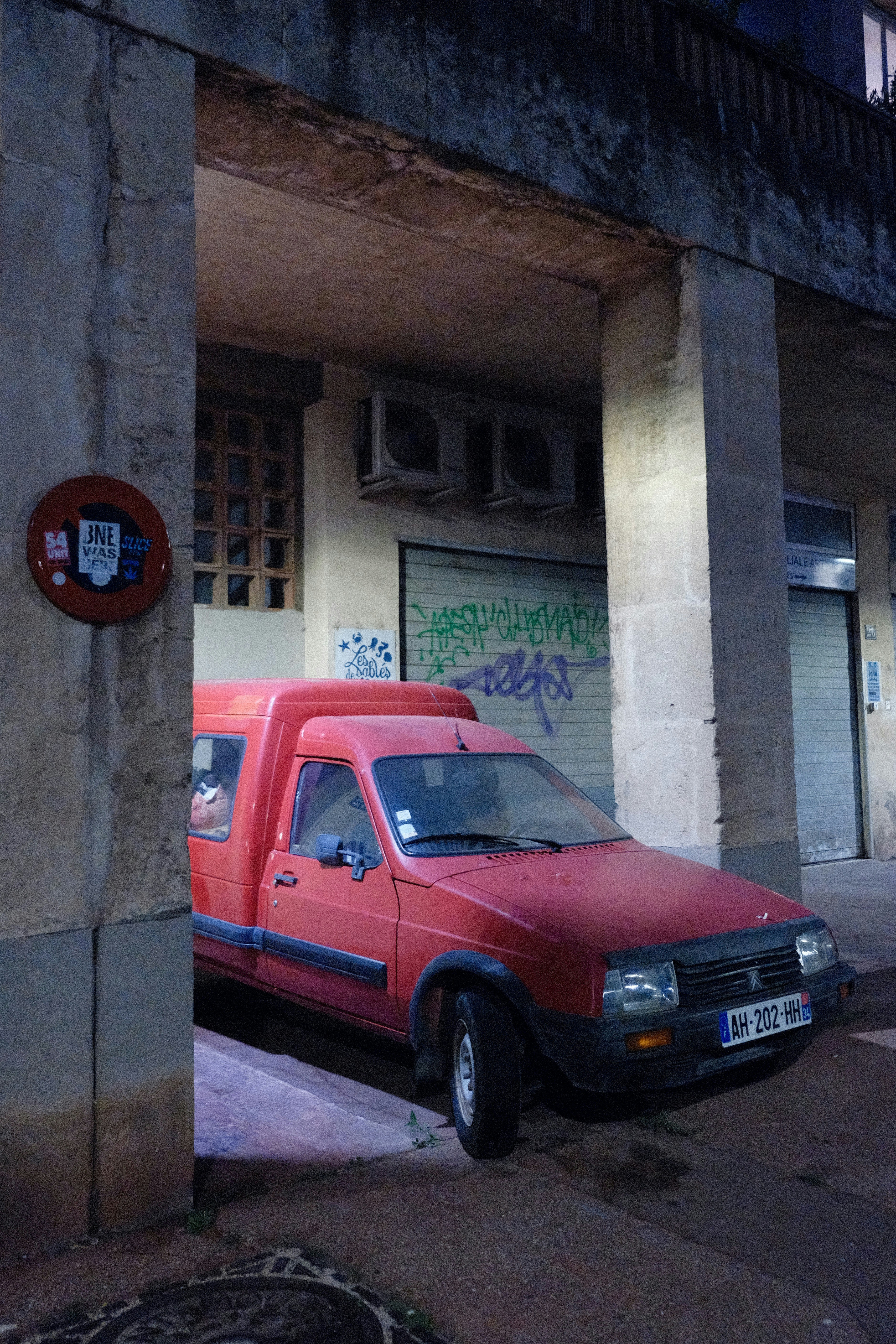 Red van parked under a concrete overhang at night.
