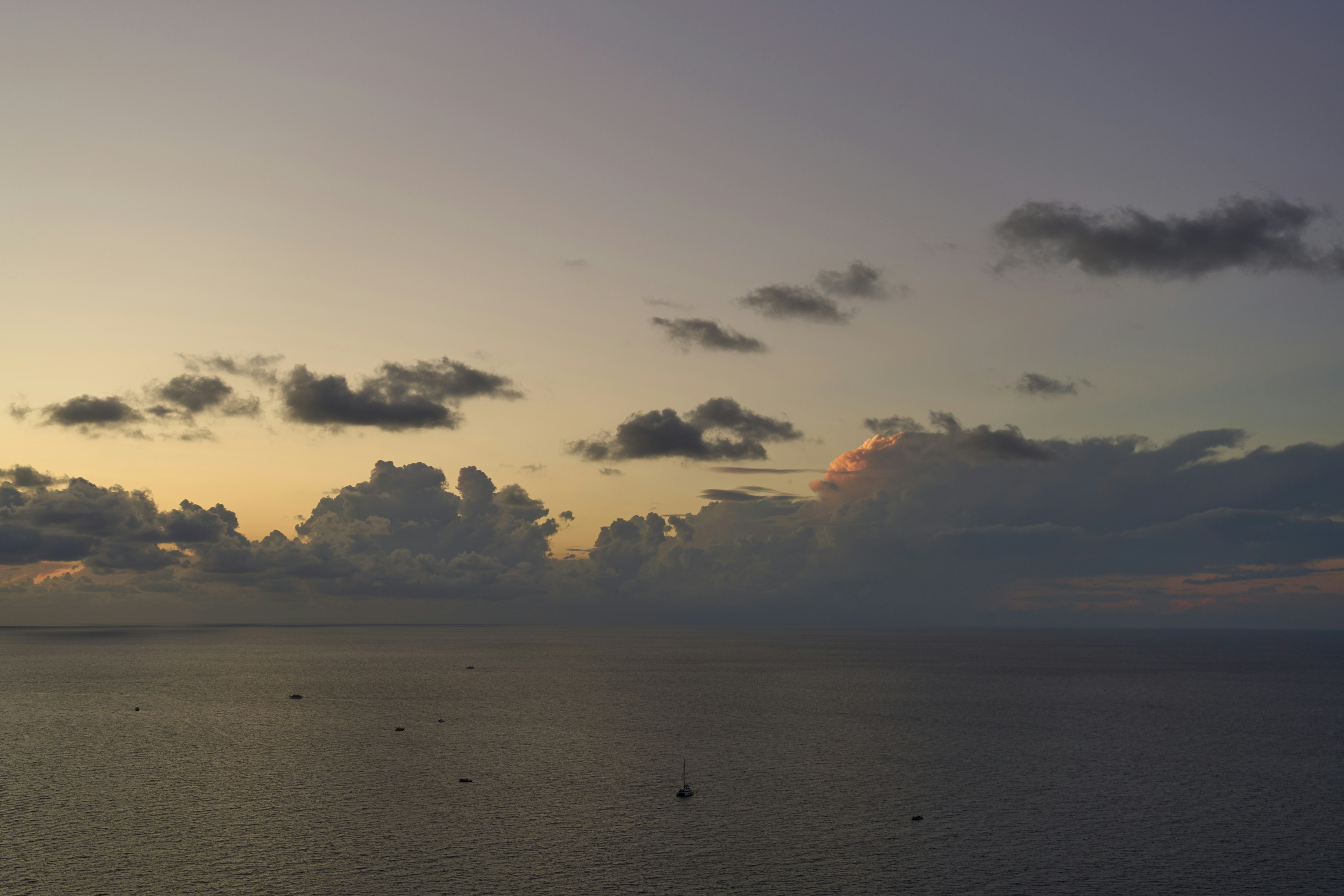 Serene seascape at twilight, featuring distant boats silhouetted against a colorful sky filled with clouds. 